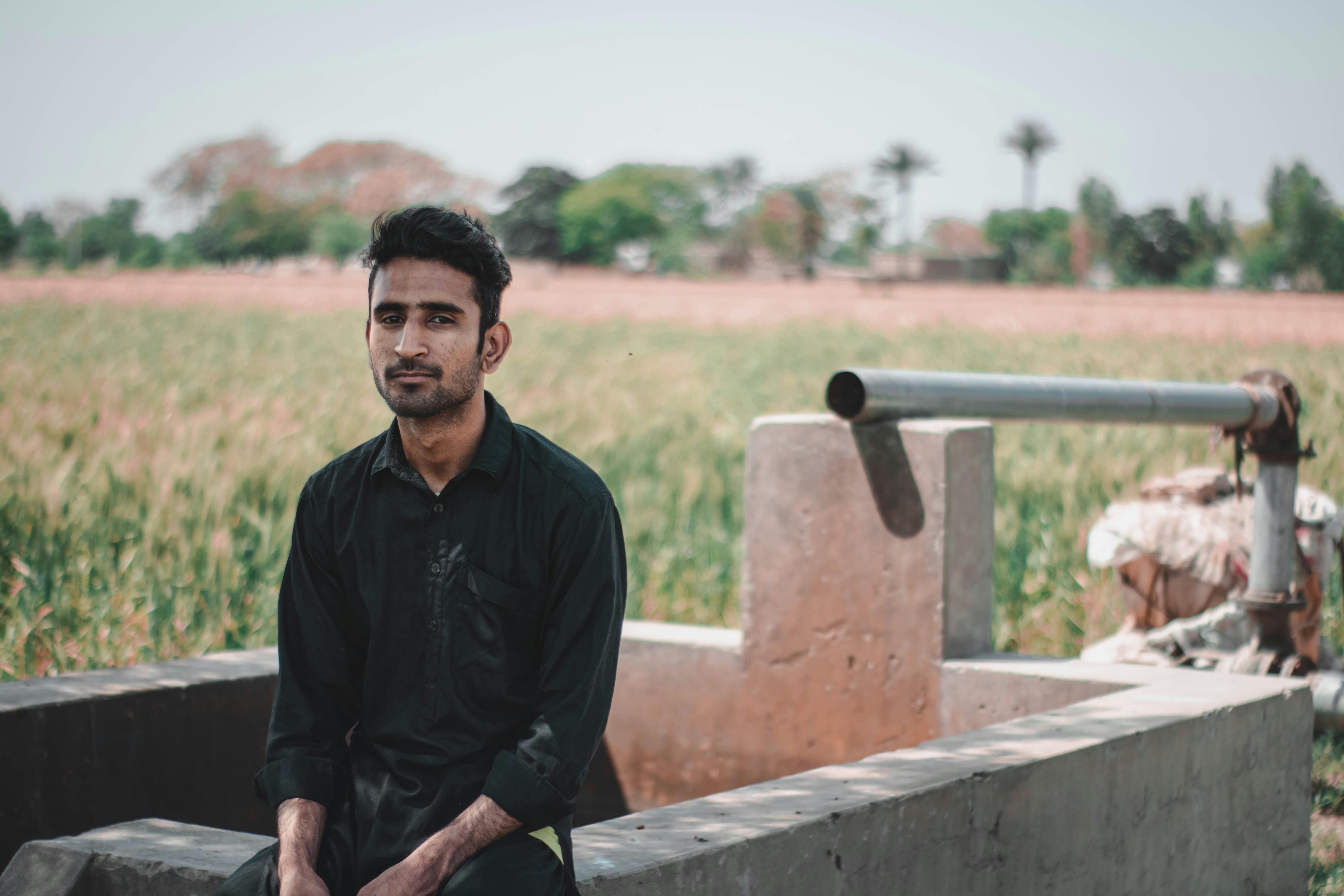 Brunette Man Sitting on a Well in a Field · Free Stock Photo
