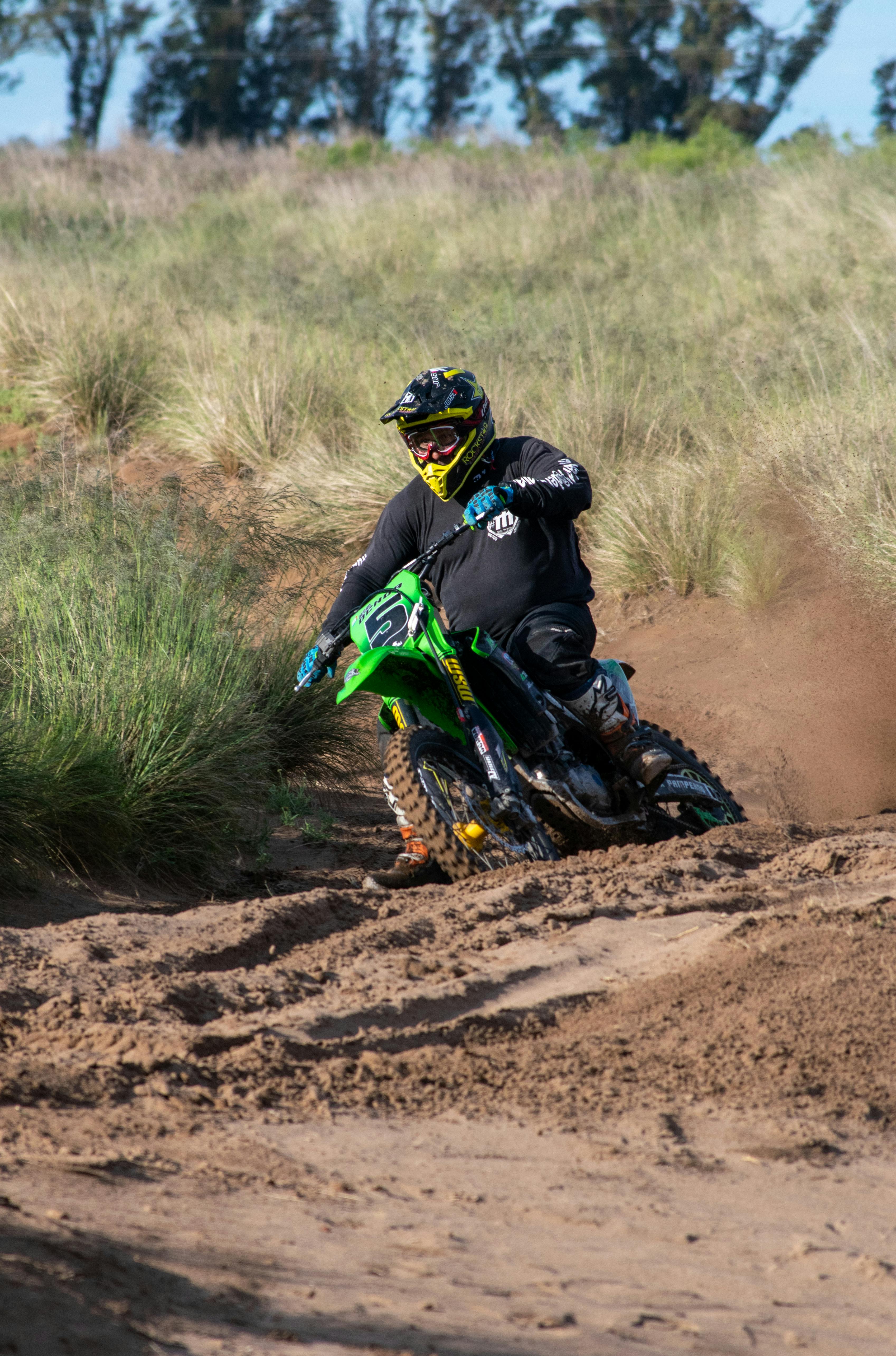 A Person Wearing a Black Racing Suit Riding a Green Motorcycle on Soil ...