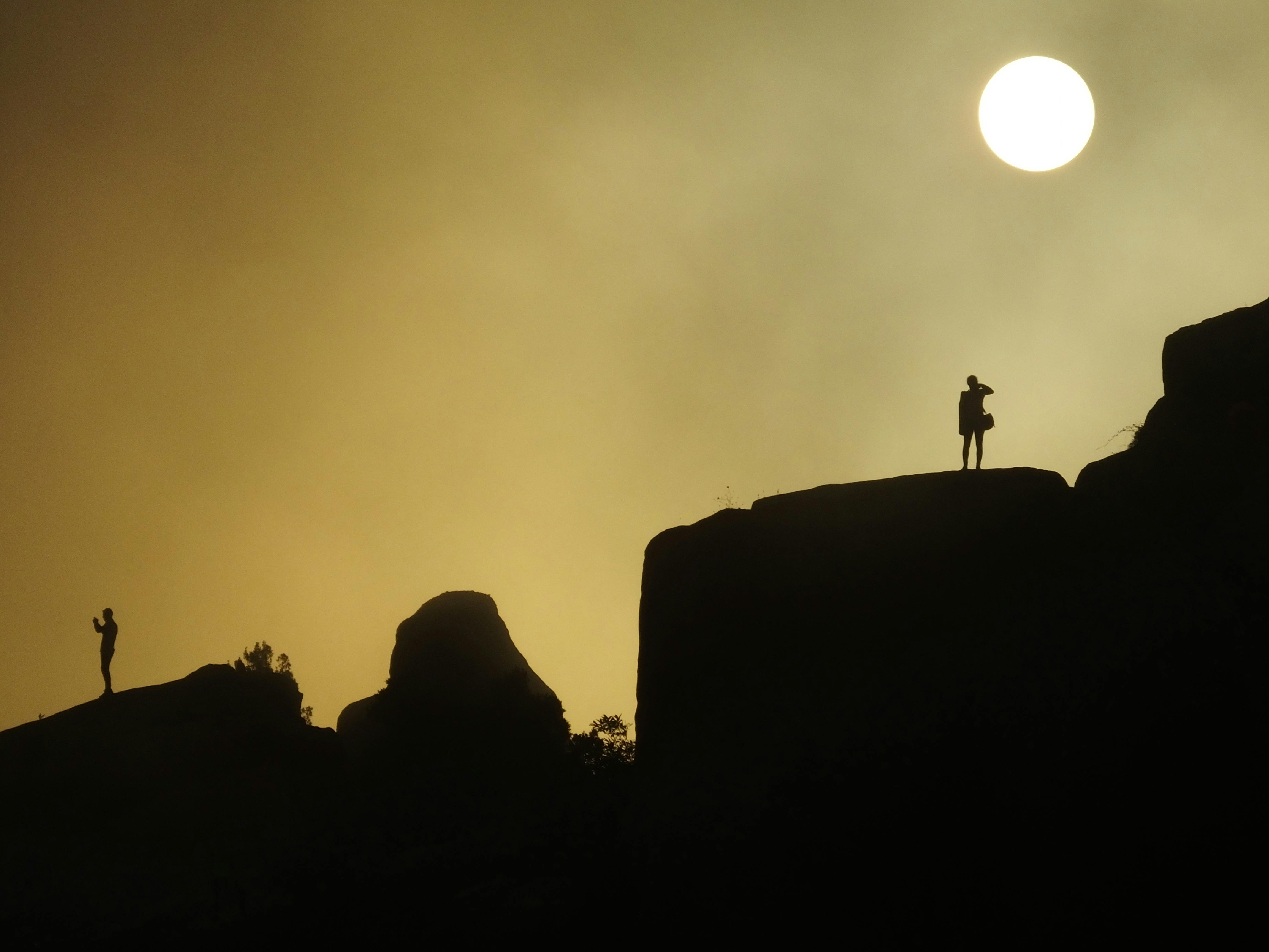 Silhouette of Person Standing on Rock Formation Under a Bright Sun ...