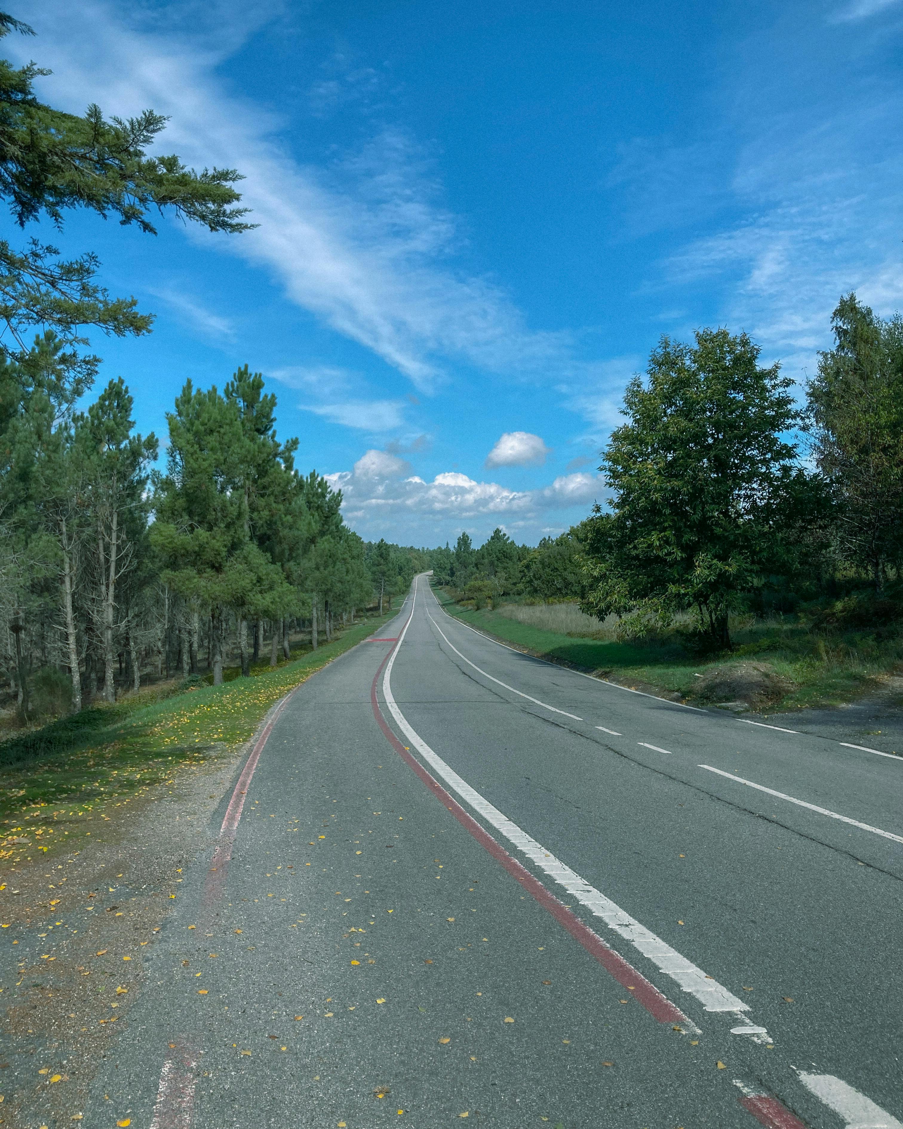 A Concrete Road Between Green Grass Field Under The Blue Sky And White