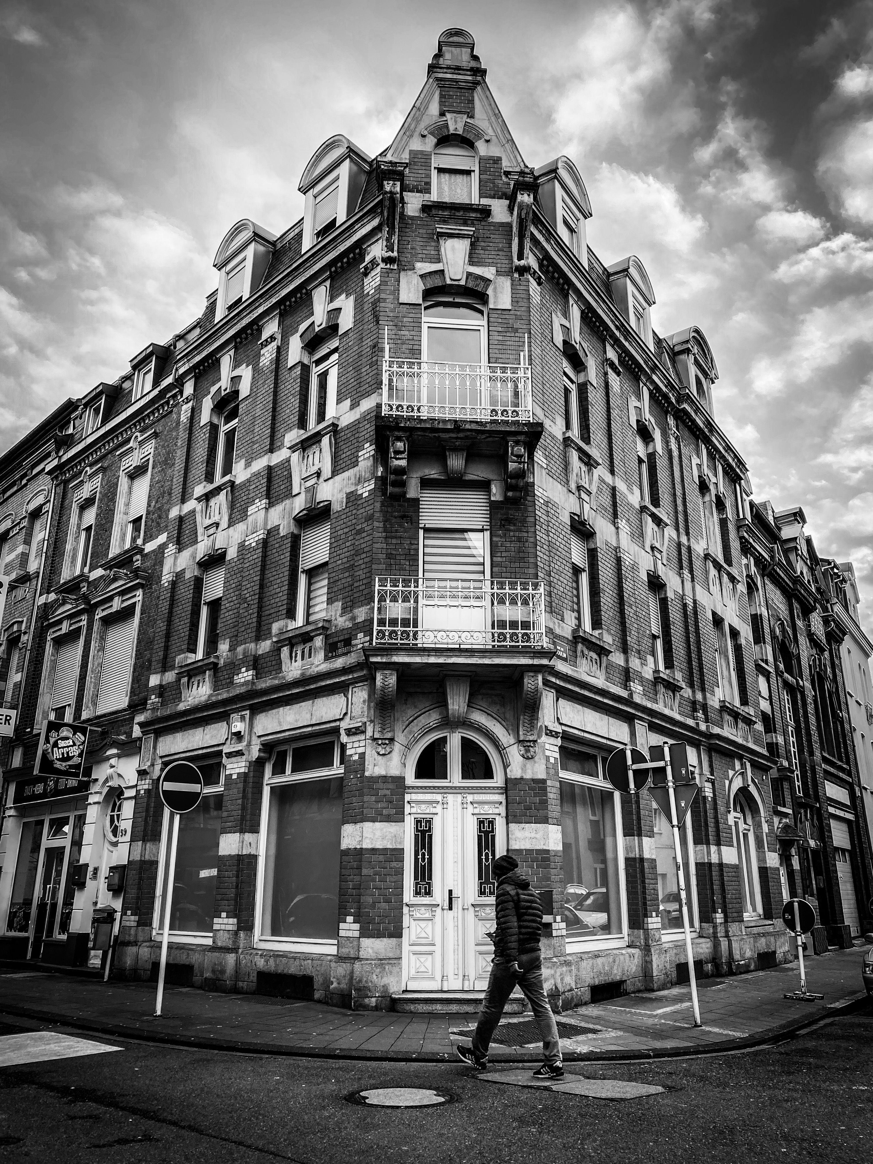 A Grayscale Photo of a Person Walking on the Street Near the Building ...