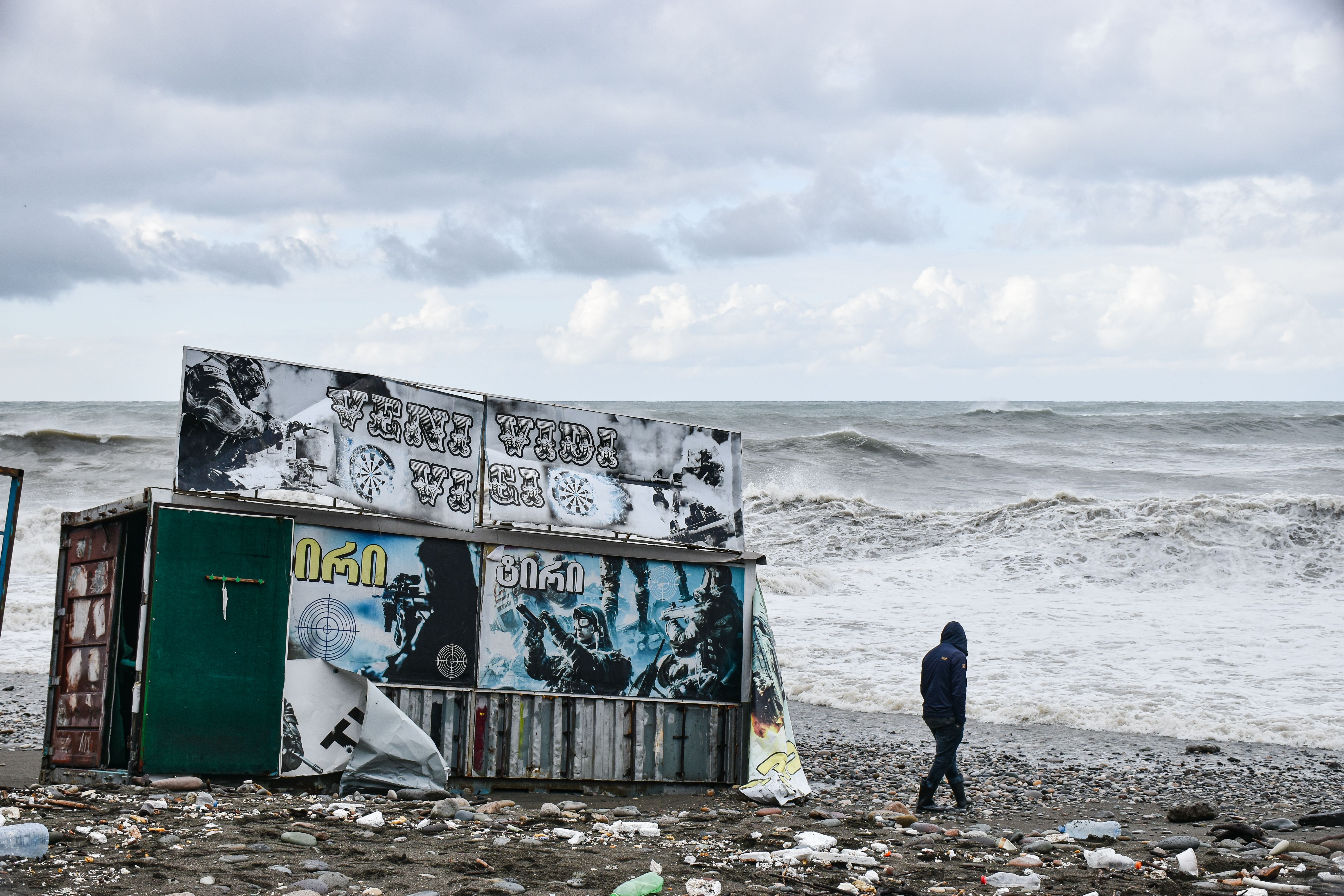 Person Walking near Trash and Shed on Beach · Free Stock Photo
