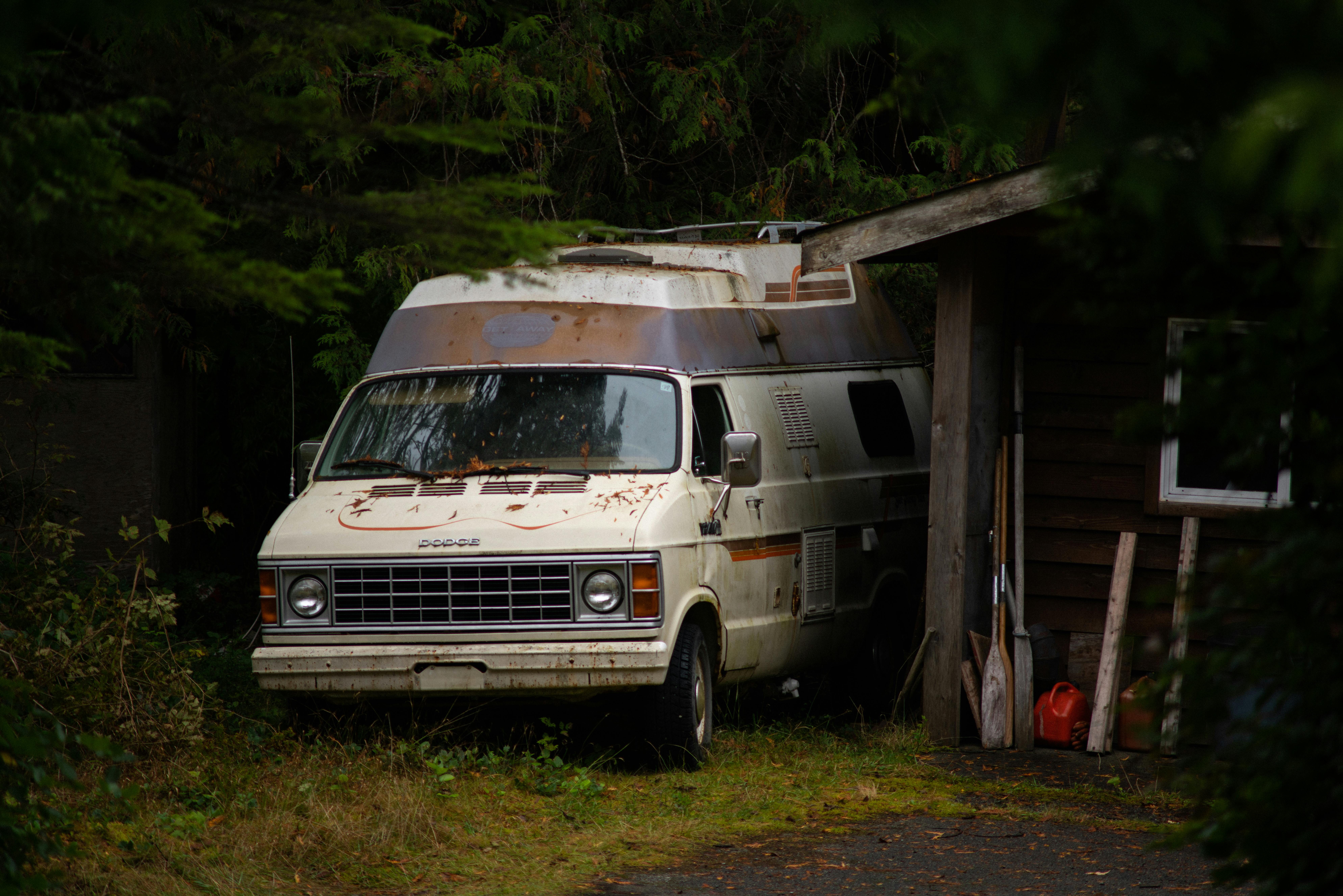 Old Camper Van Parked Near Wooden House and Green Trees · Free Stock Photo