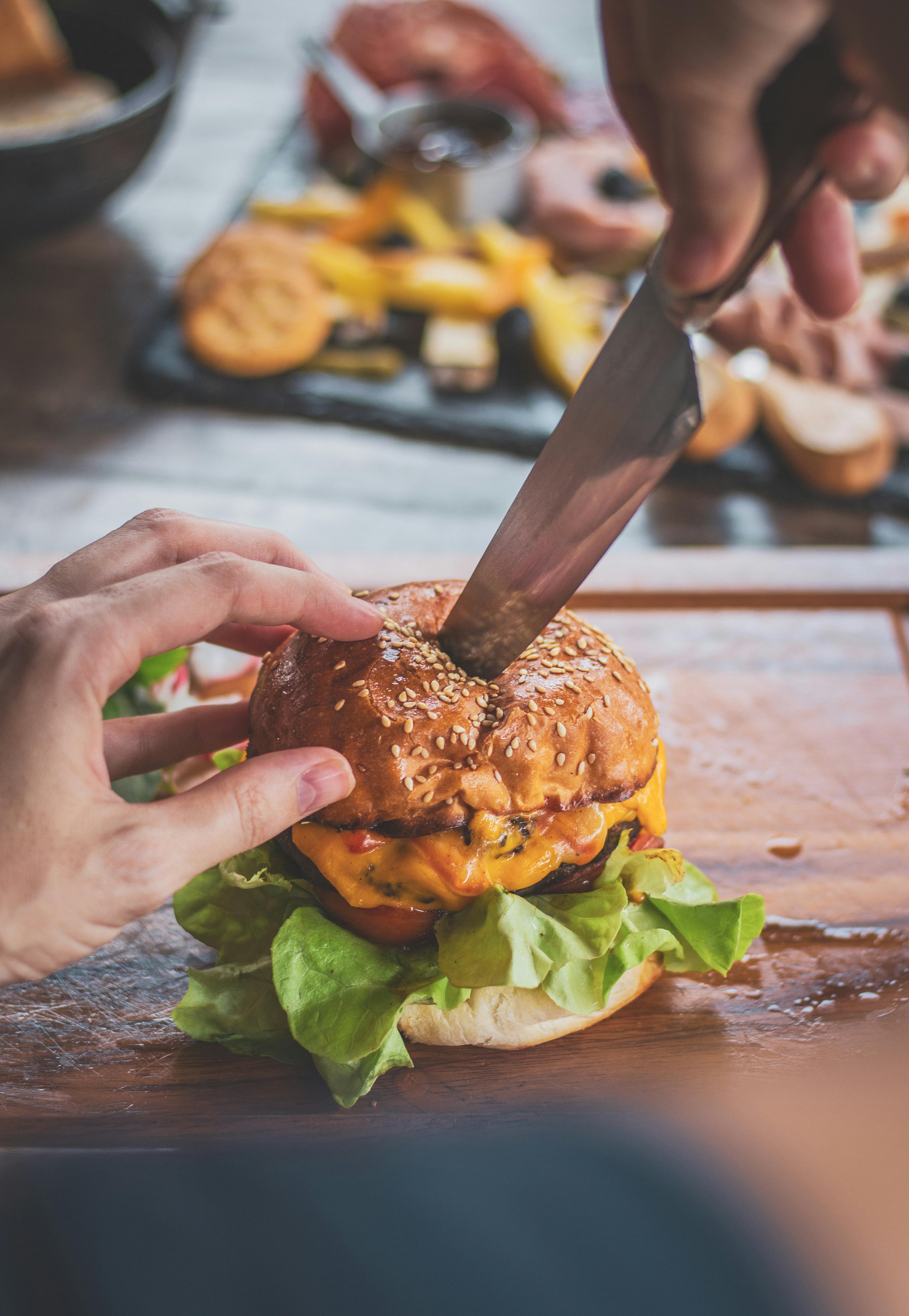 Person Cutting Cheeseburger with a Kitchen Knife · Free Stock Photo
