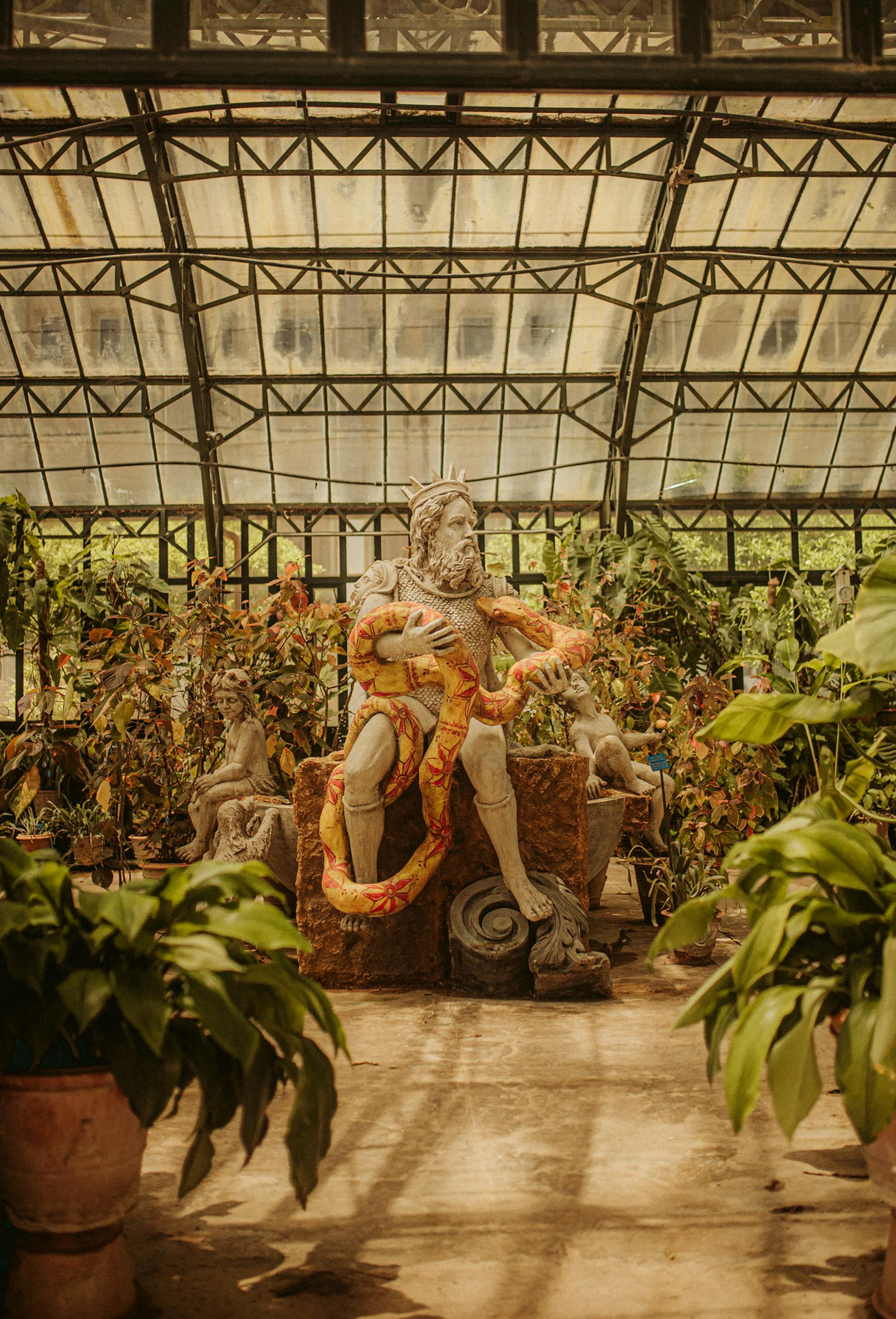 Statue of Man Holding Snake inside Greenhouse · Free Stock Photo