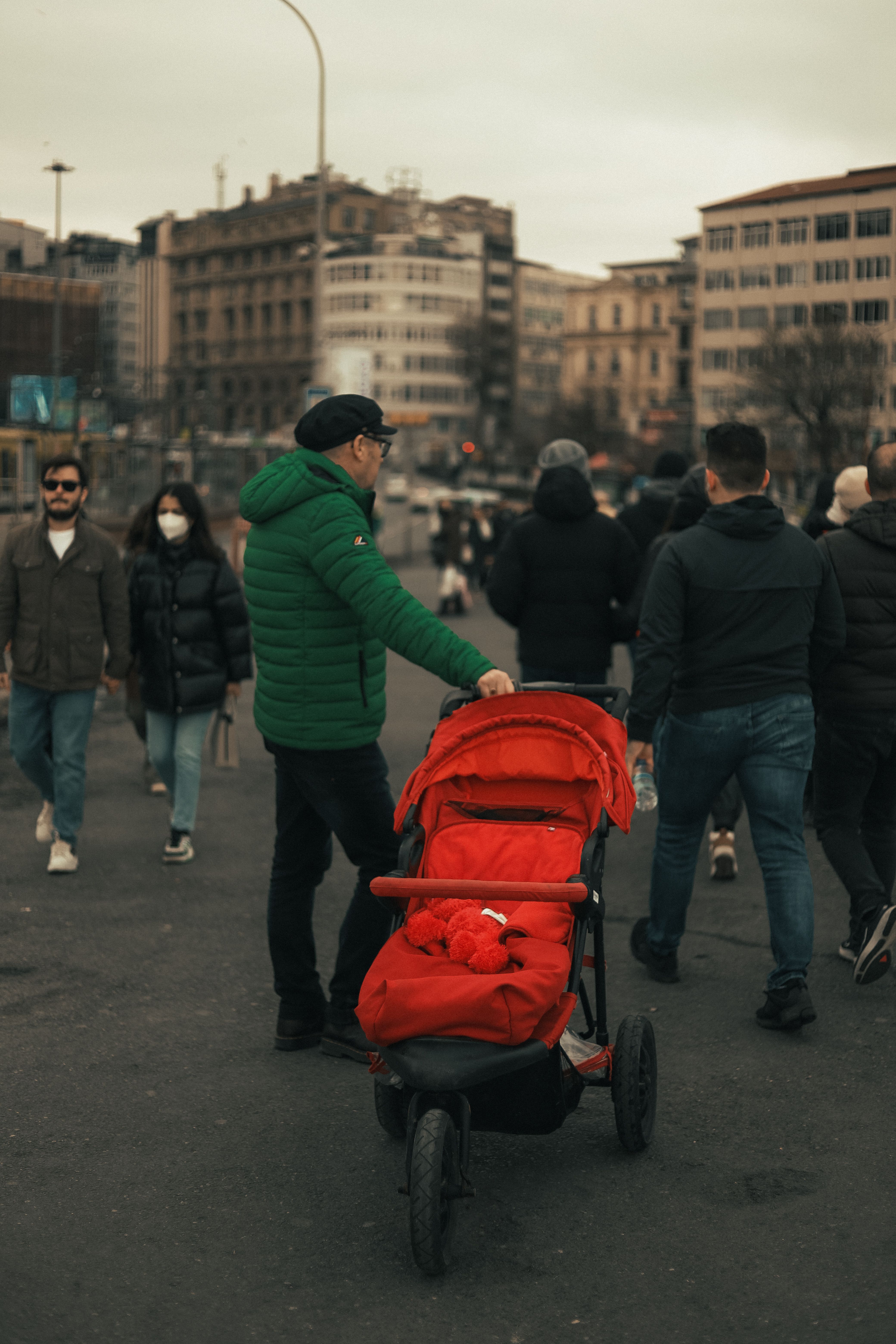 Man in Green Jacket Holding a Red Baby Stroller · Free Stock Photo