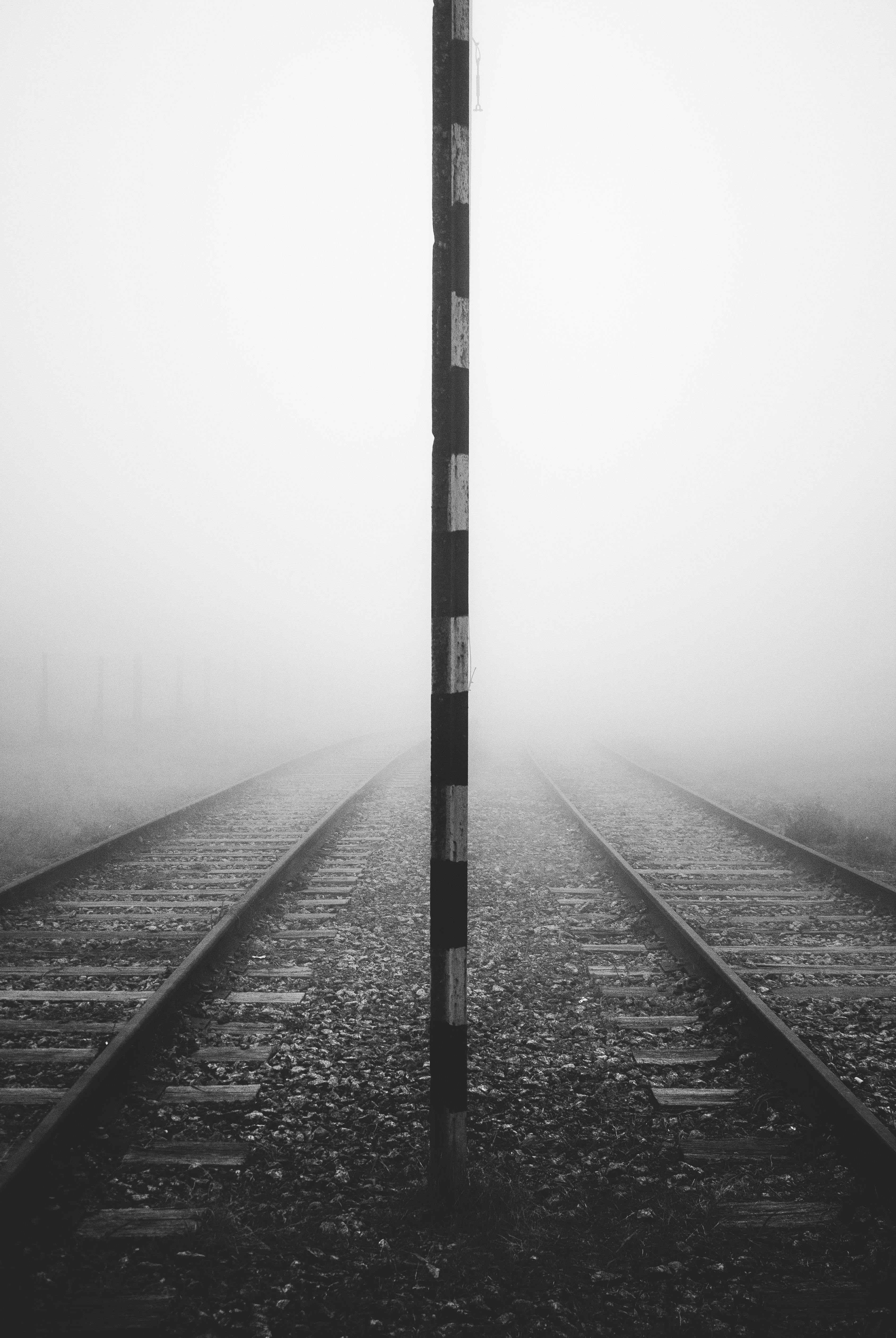 A Grayscale Photo of a Post Between Train Tracks · Free Stock Photo