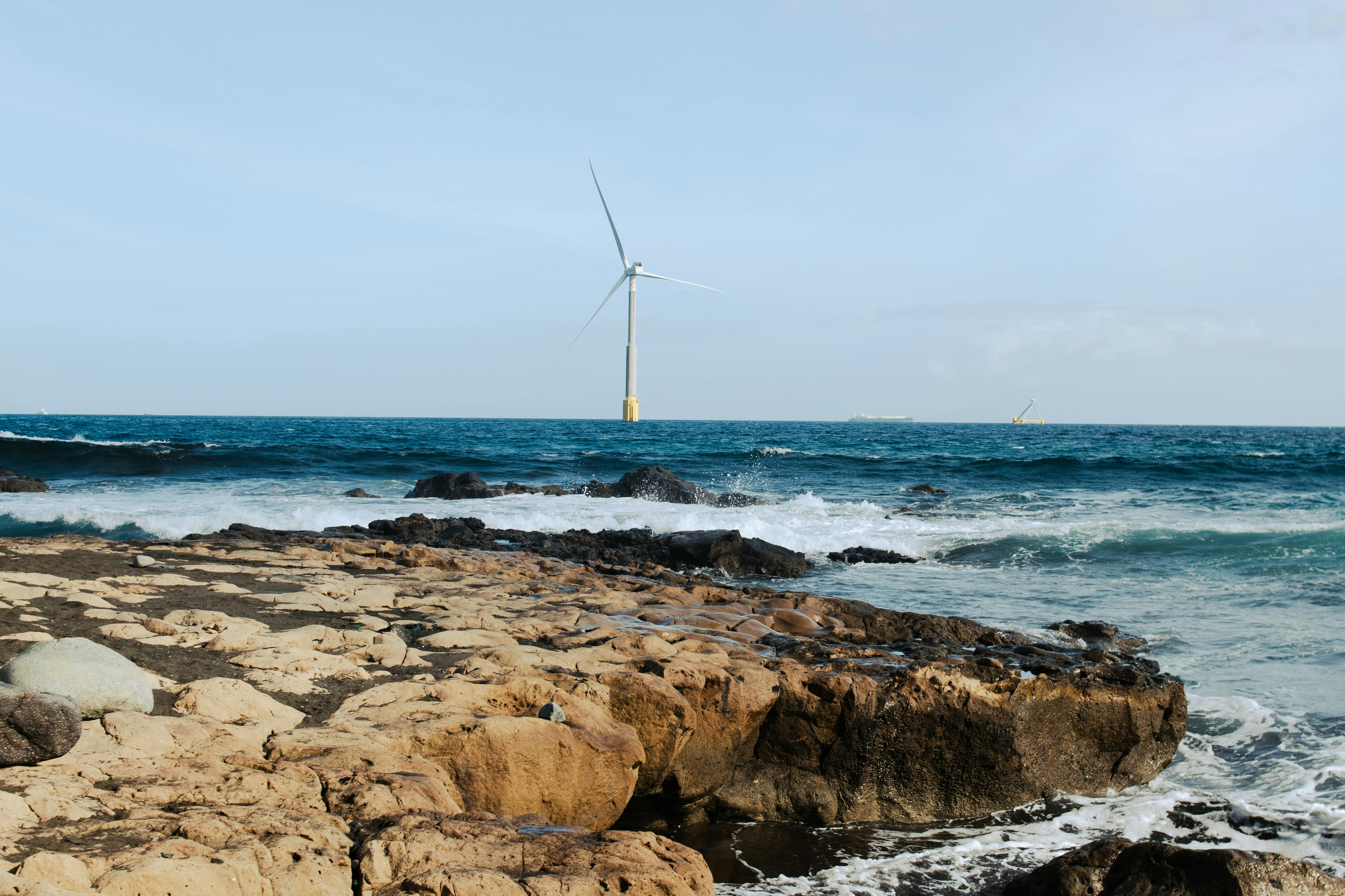 Rocks on Sea Shore with Wind Turbine behind · Free Stock Photo