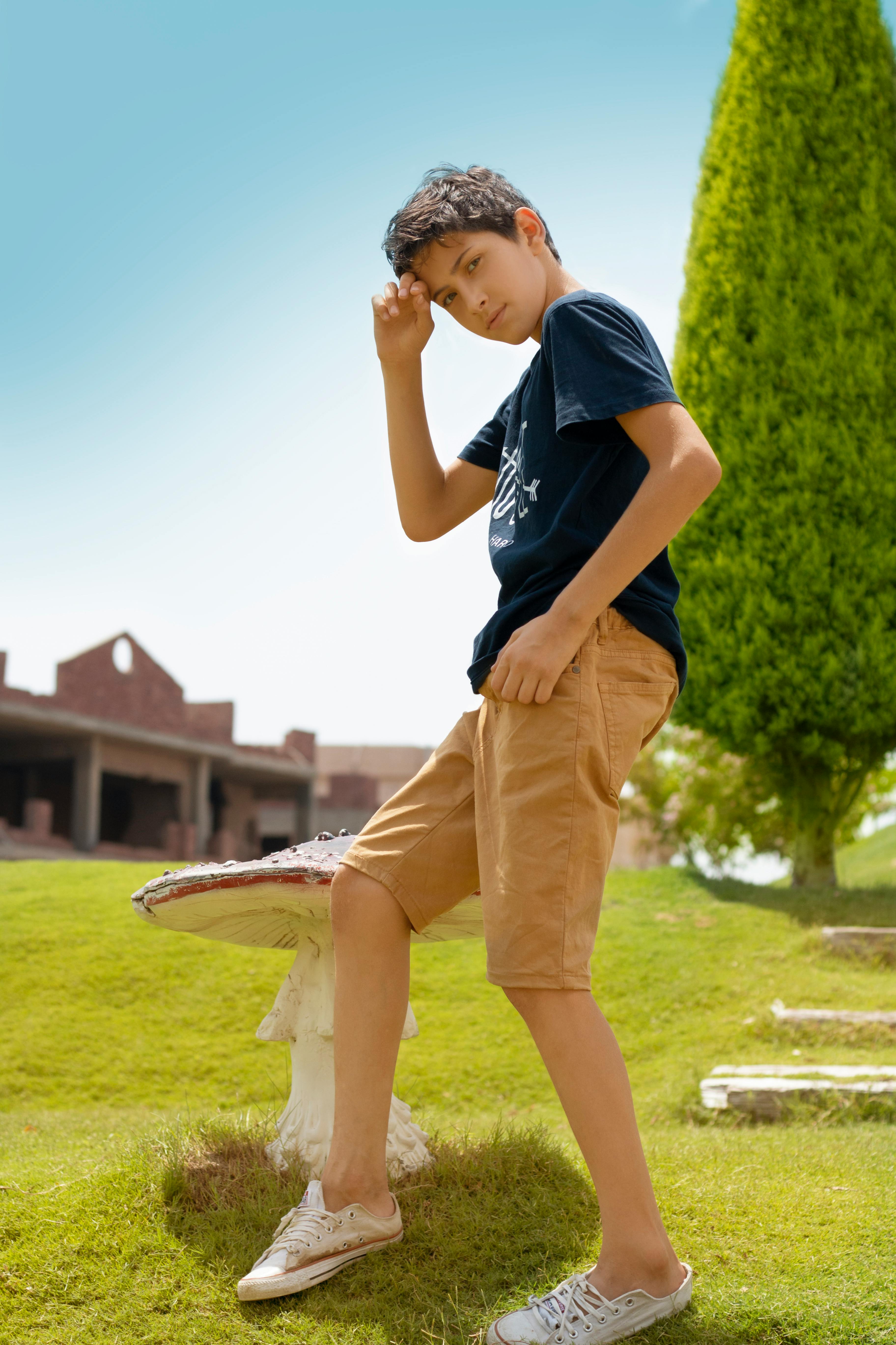 A boy in shorts and a hat is standing on a grassy area · Free Stock Photo