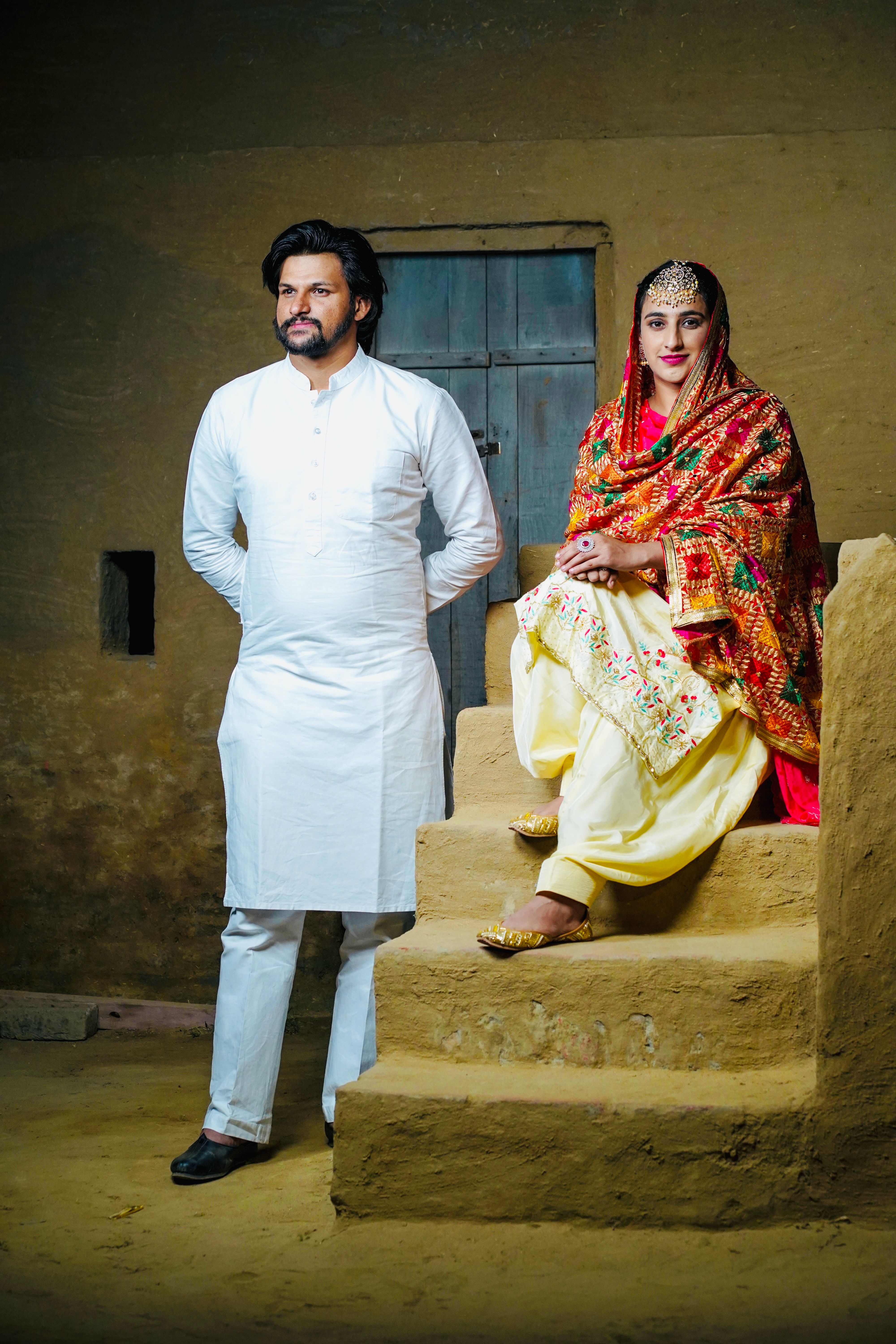 A Man in White Sherwani Standing Beside the Woman Sitting on a Concrete ...