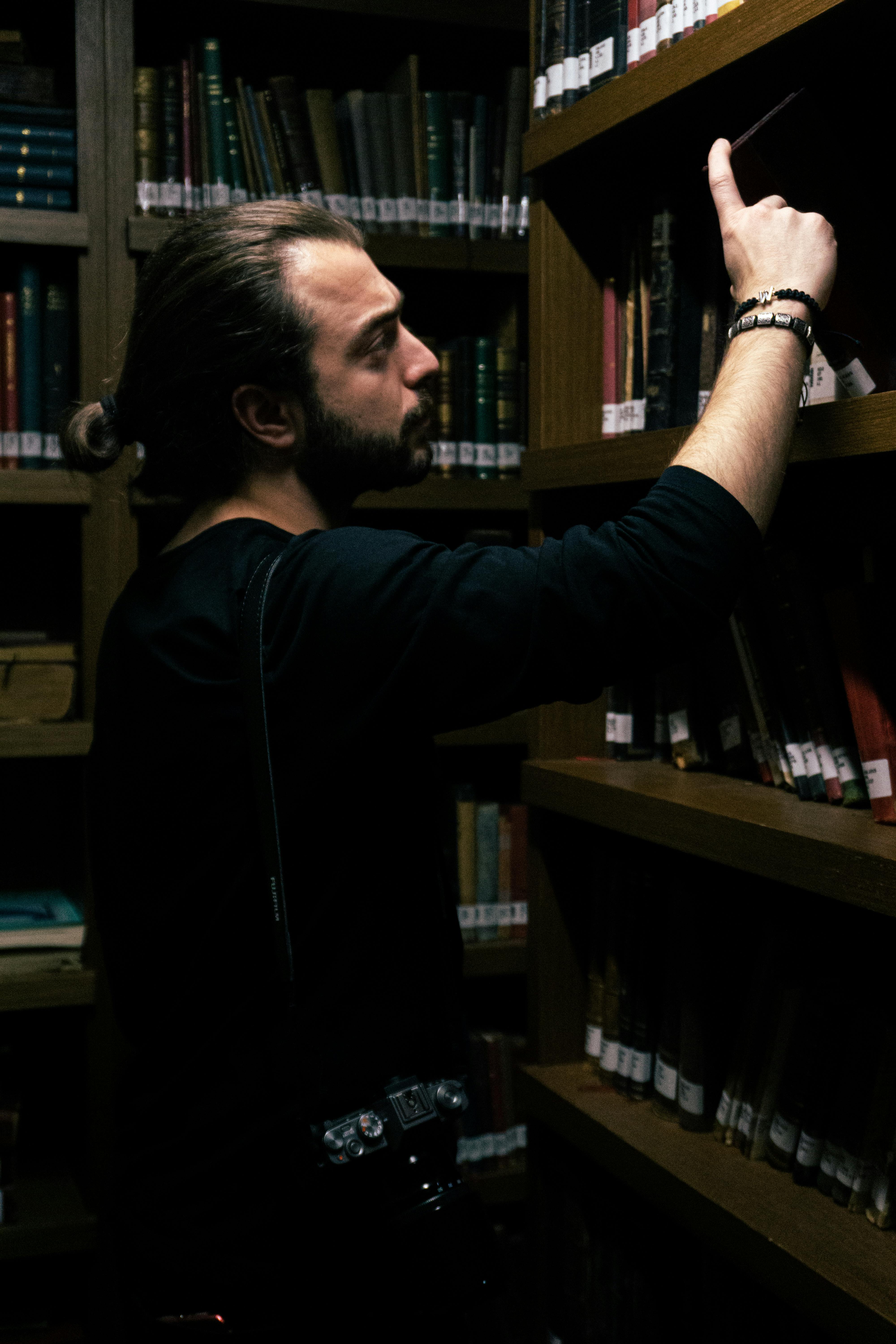 A Bearded Man Getting a Book from a Bookshelf · Free Stock Photo