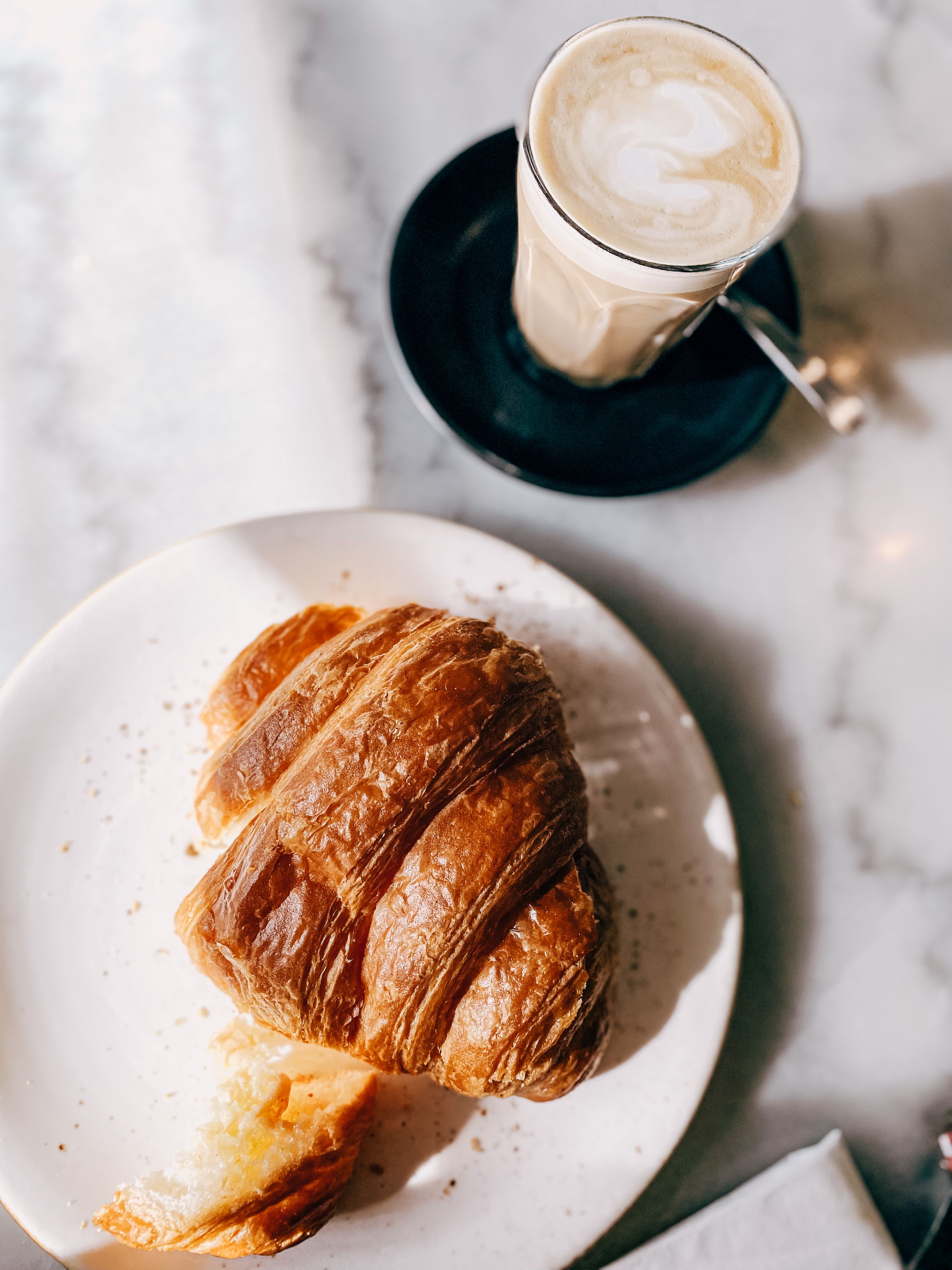 A Close-Up Shot of a Croissant beside a Glass of Coffee · Free Stock Photo