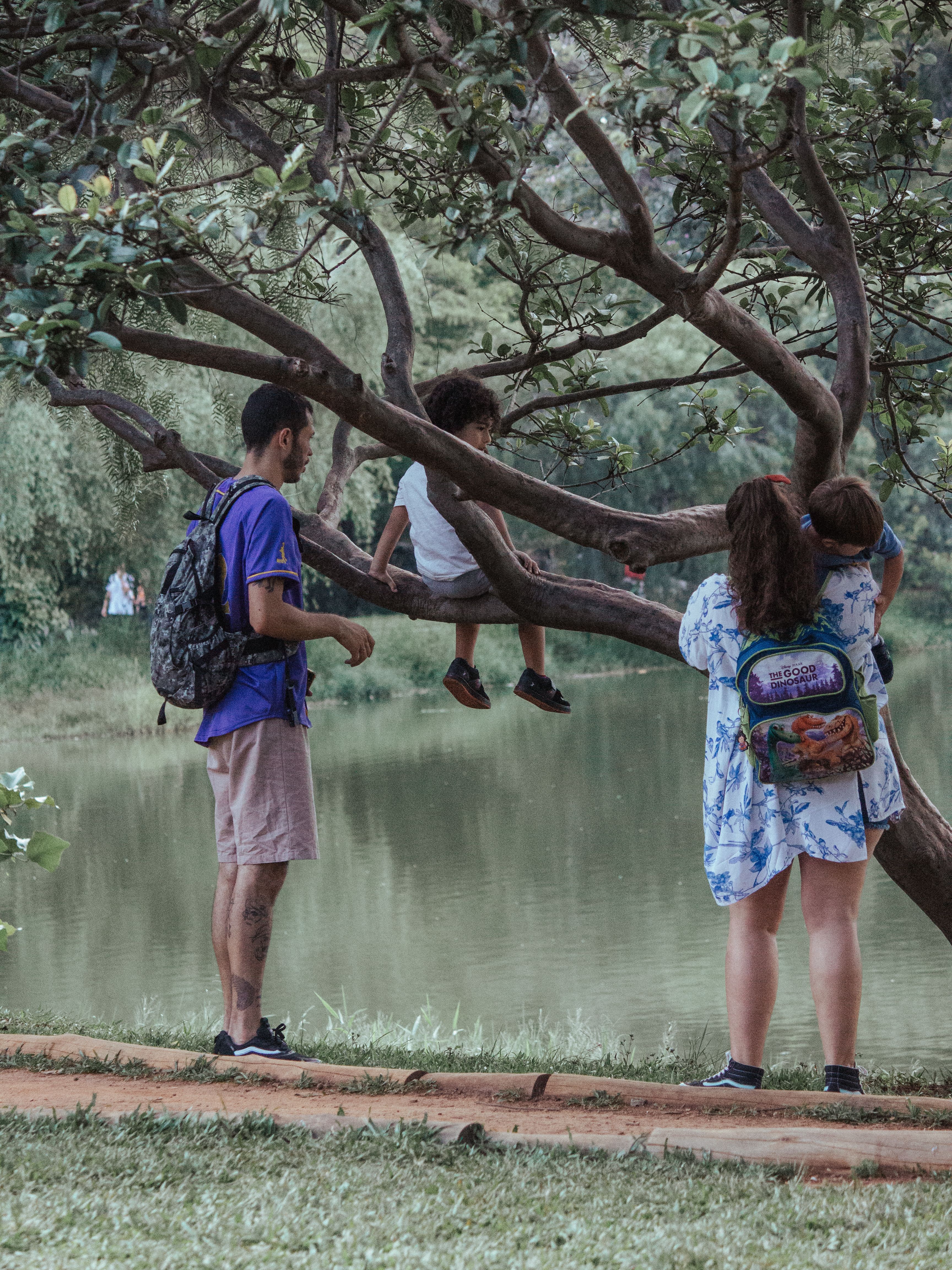 Family with Two Kids Standing by a Tree by a Pond · Free Stock Photo