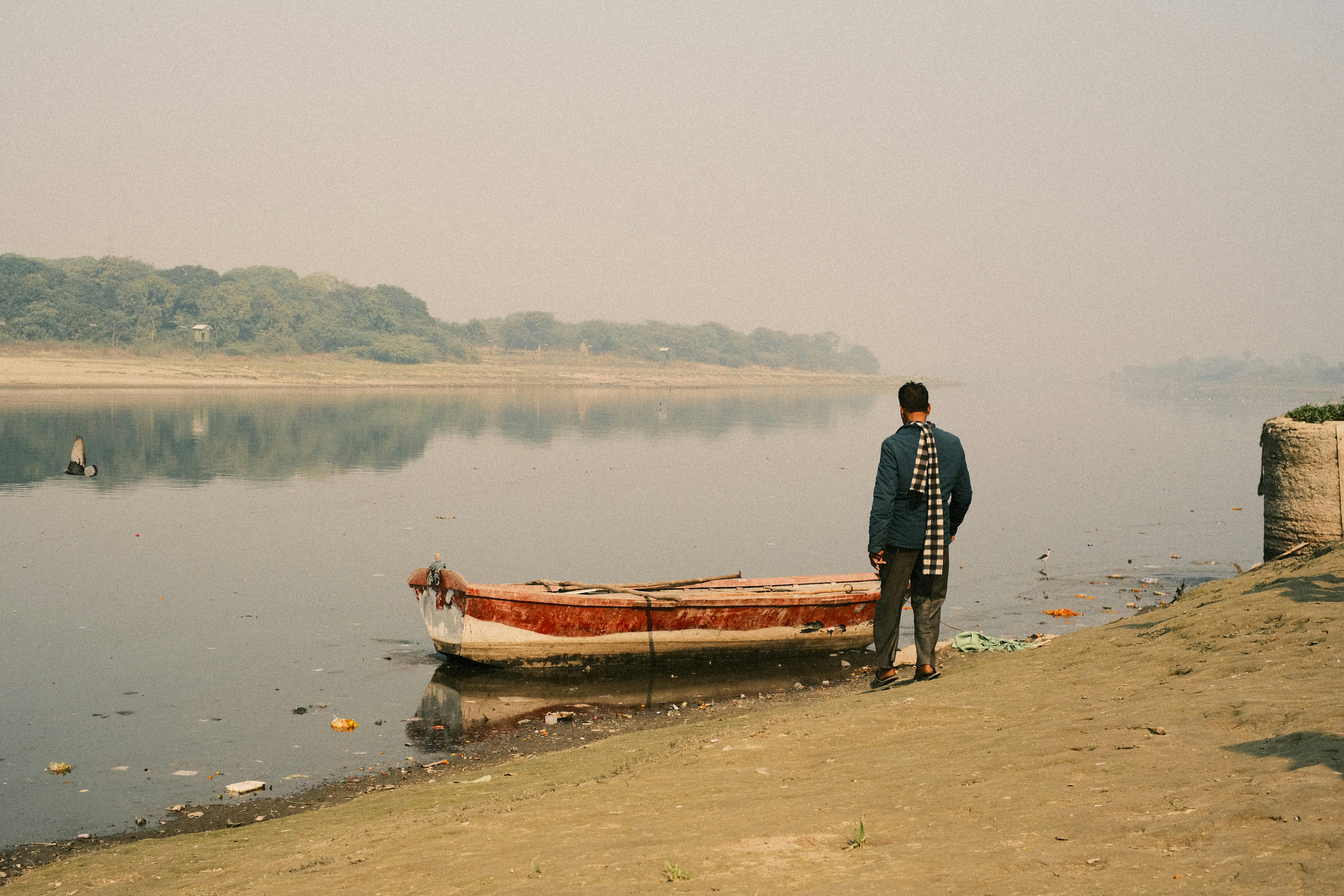 Man Standing by Boat on River in Village · Free Stock Photo