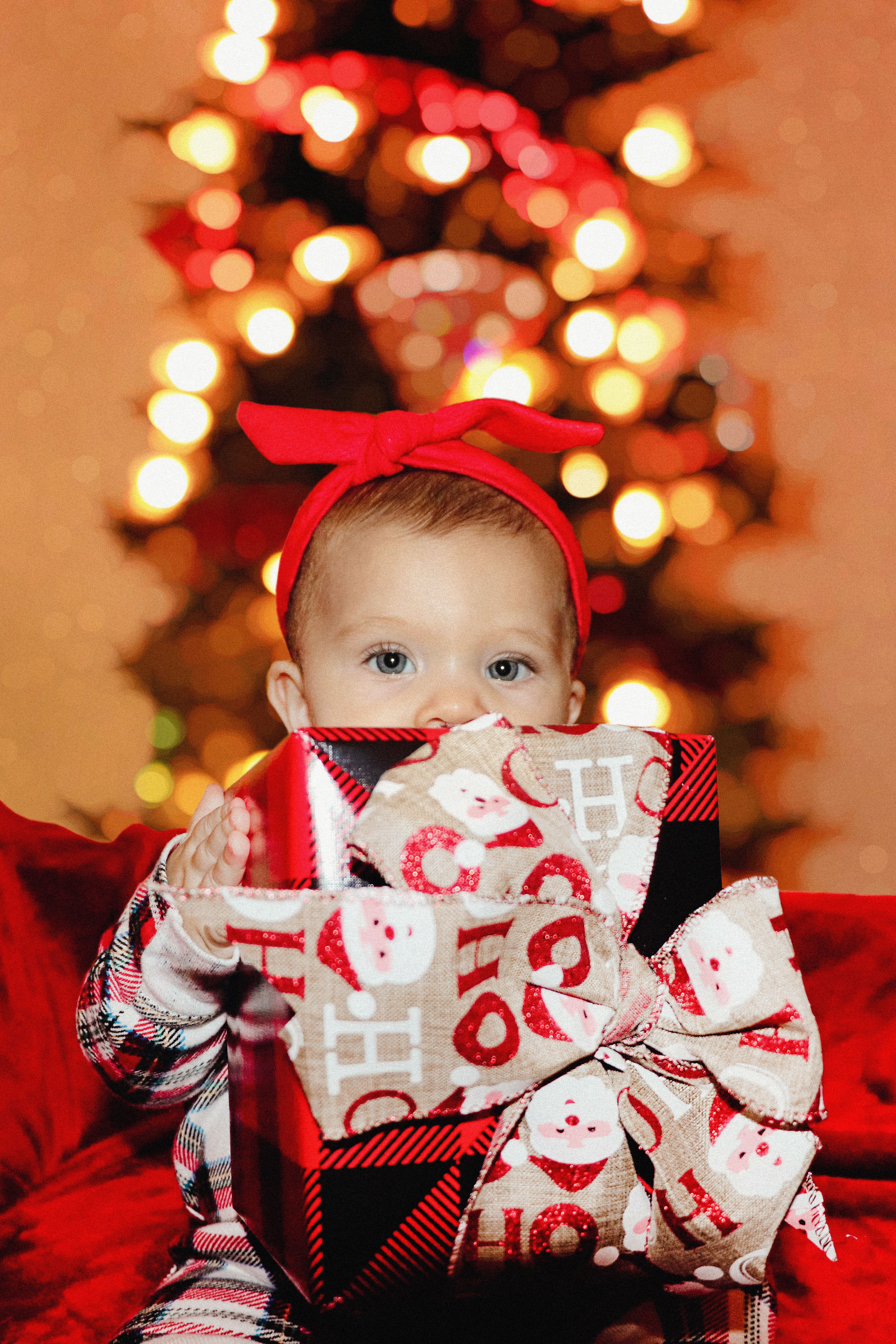 A baby girl holding a christmas present in front of a christmas tree ...