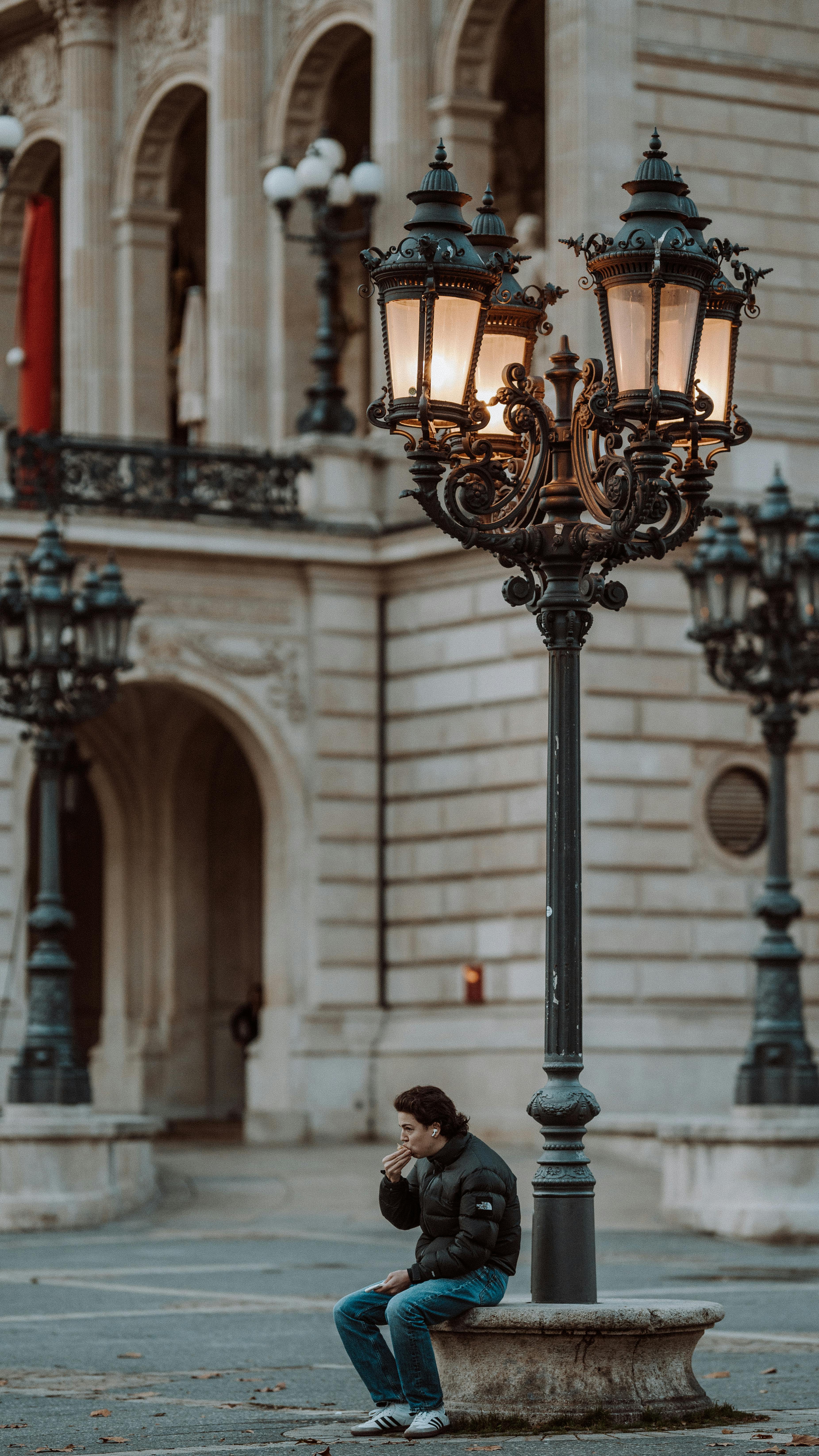 Man in Black Puffer Jacket Sitting Under the Lamp Post · Free Stock Photo