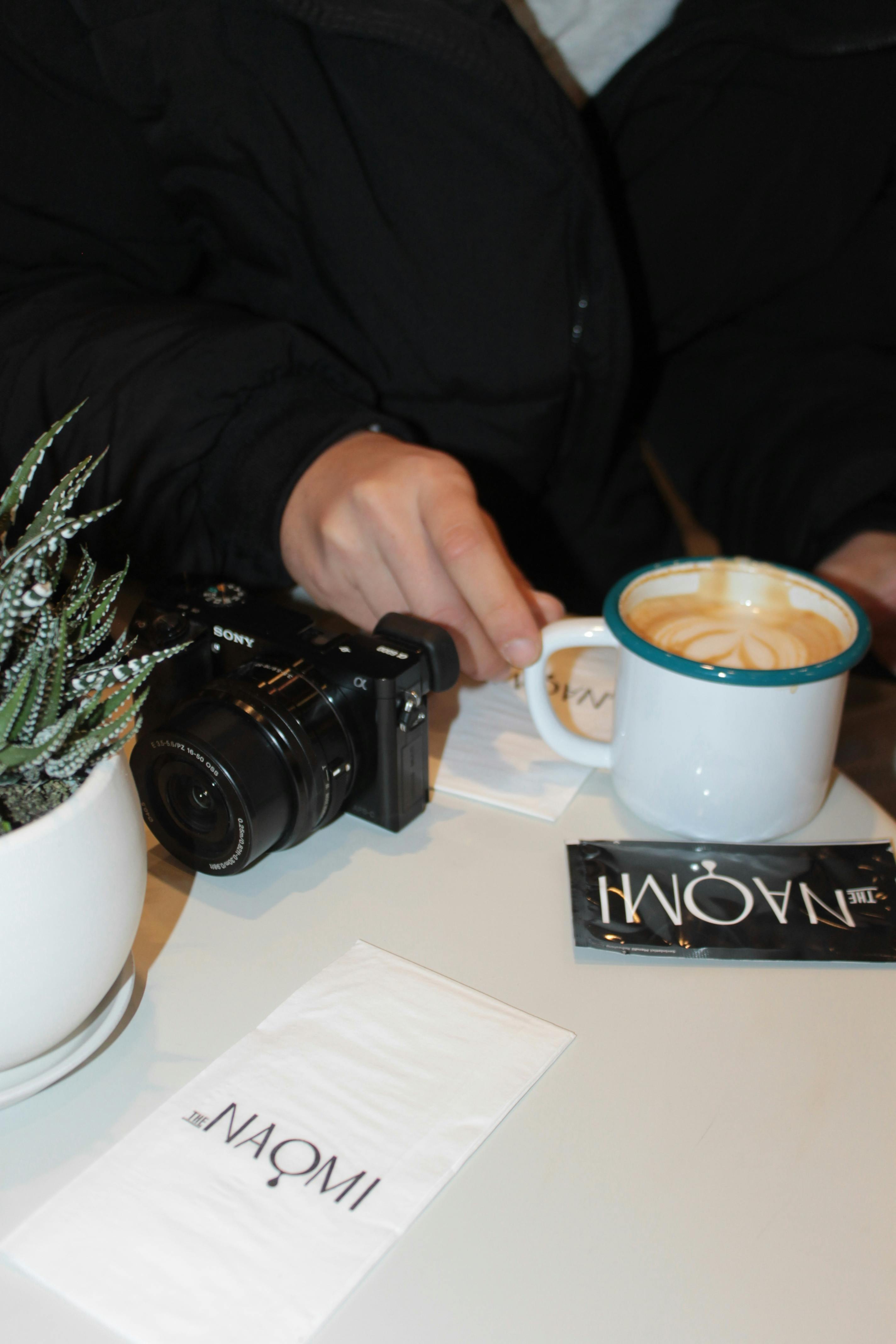 Person Sitting by Table with Coffee and Camera · Free Stock Photo