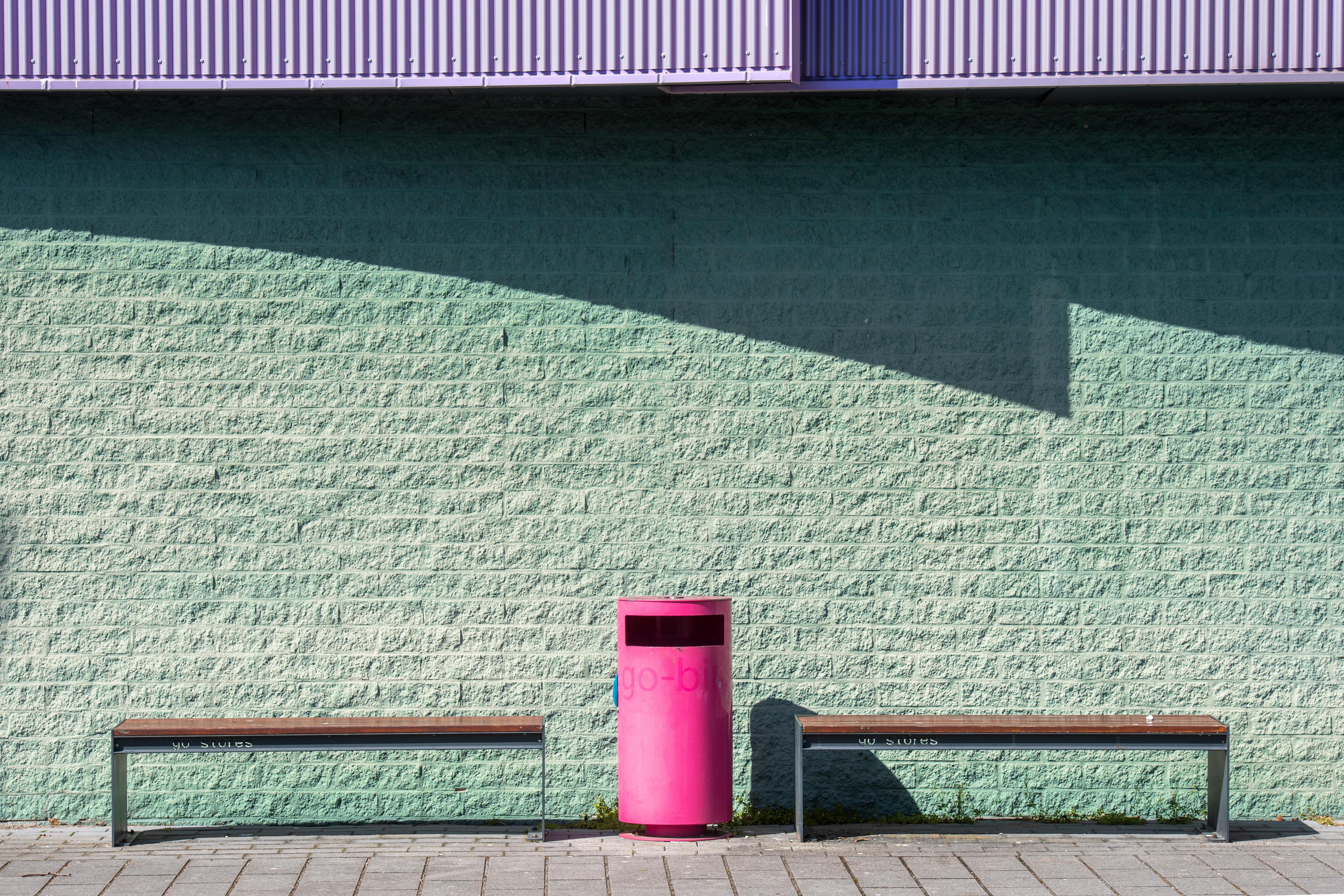 Pink Garbage Bin Between Two Benches Beside Green Wall · Free Stock Photo