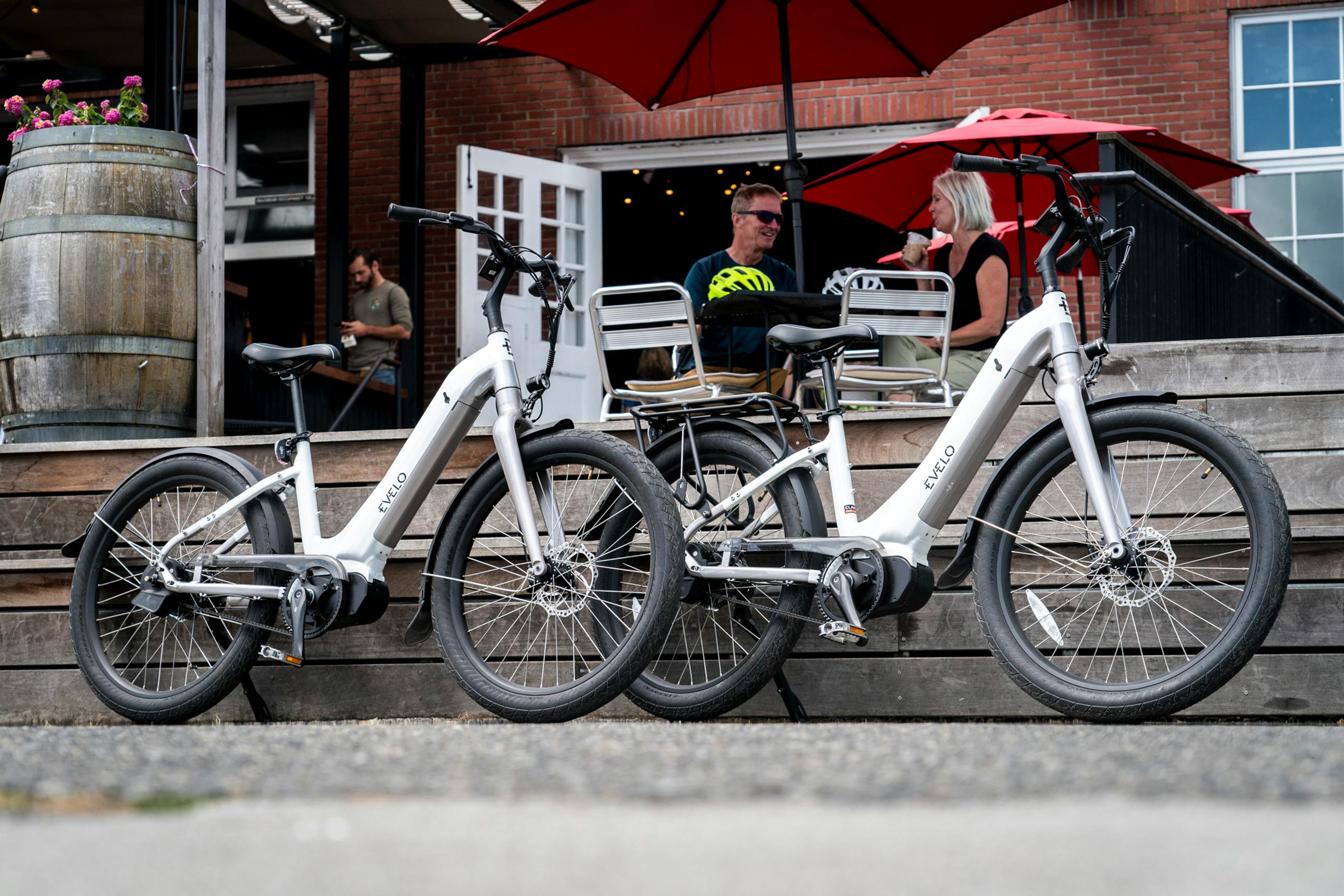A Pair of White Electric Bikes Parked Near Couple Sitting Outside a ...