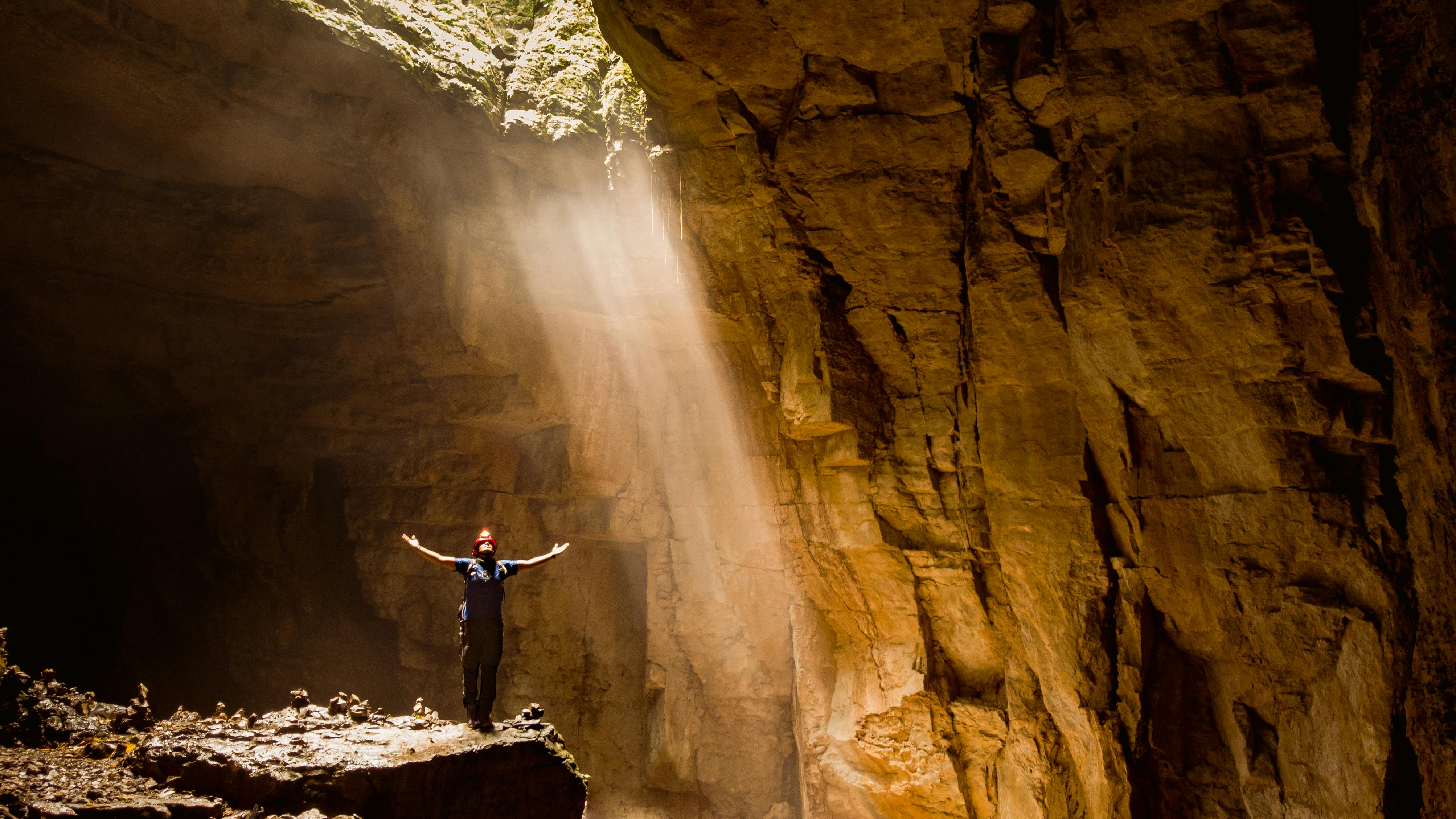 Man Standing on a Rock in a Cave with Outstretched Arms · Free Stock Photo