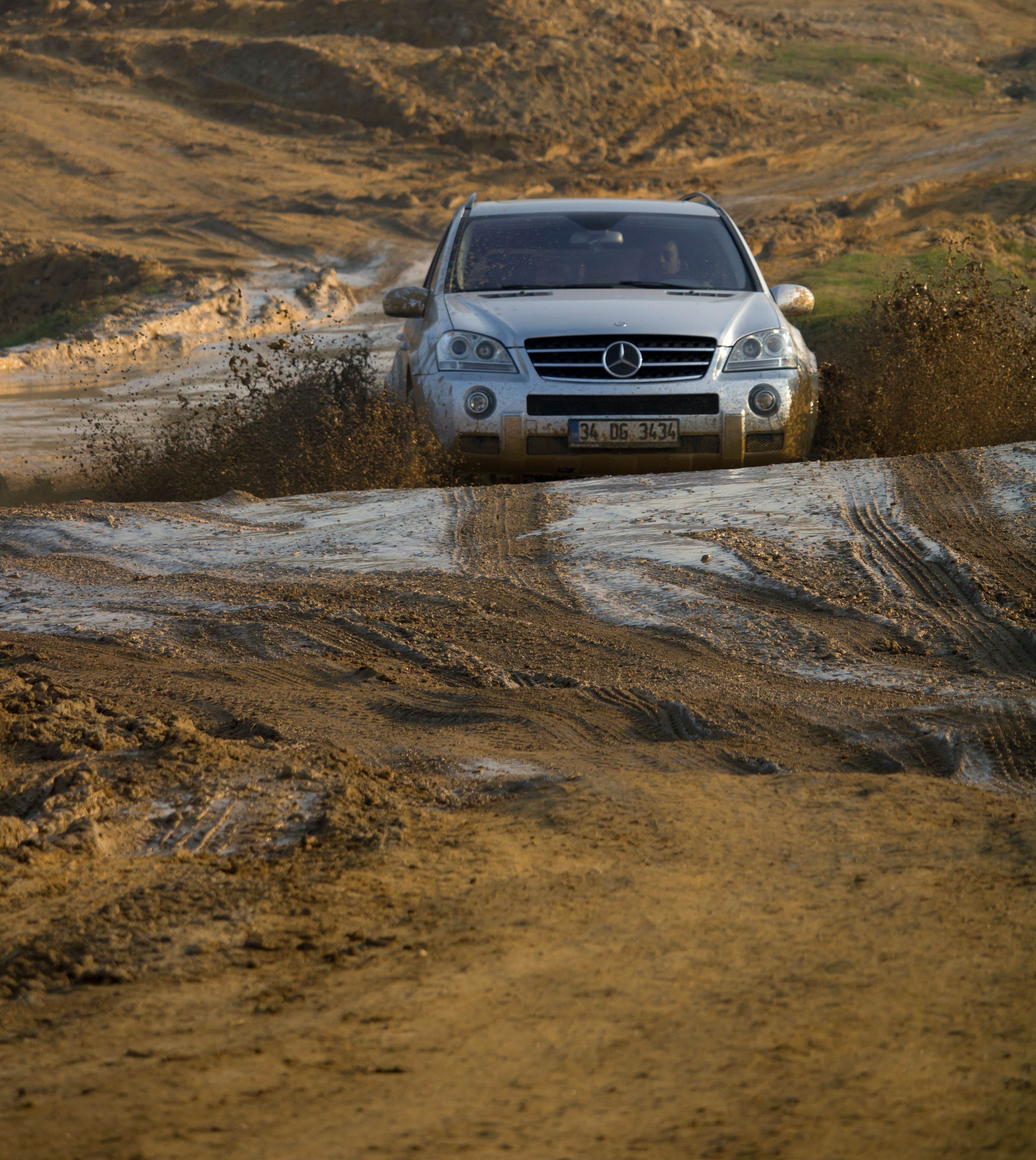 A Mercedes Driving on a Dirt Road and Splashing Mud · Free Stock Photo