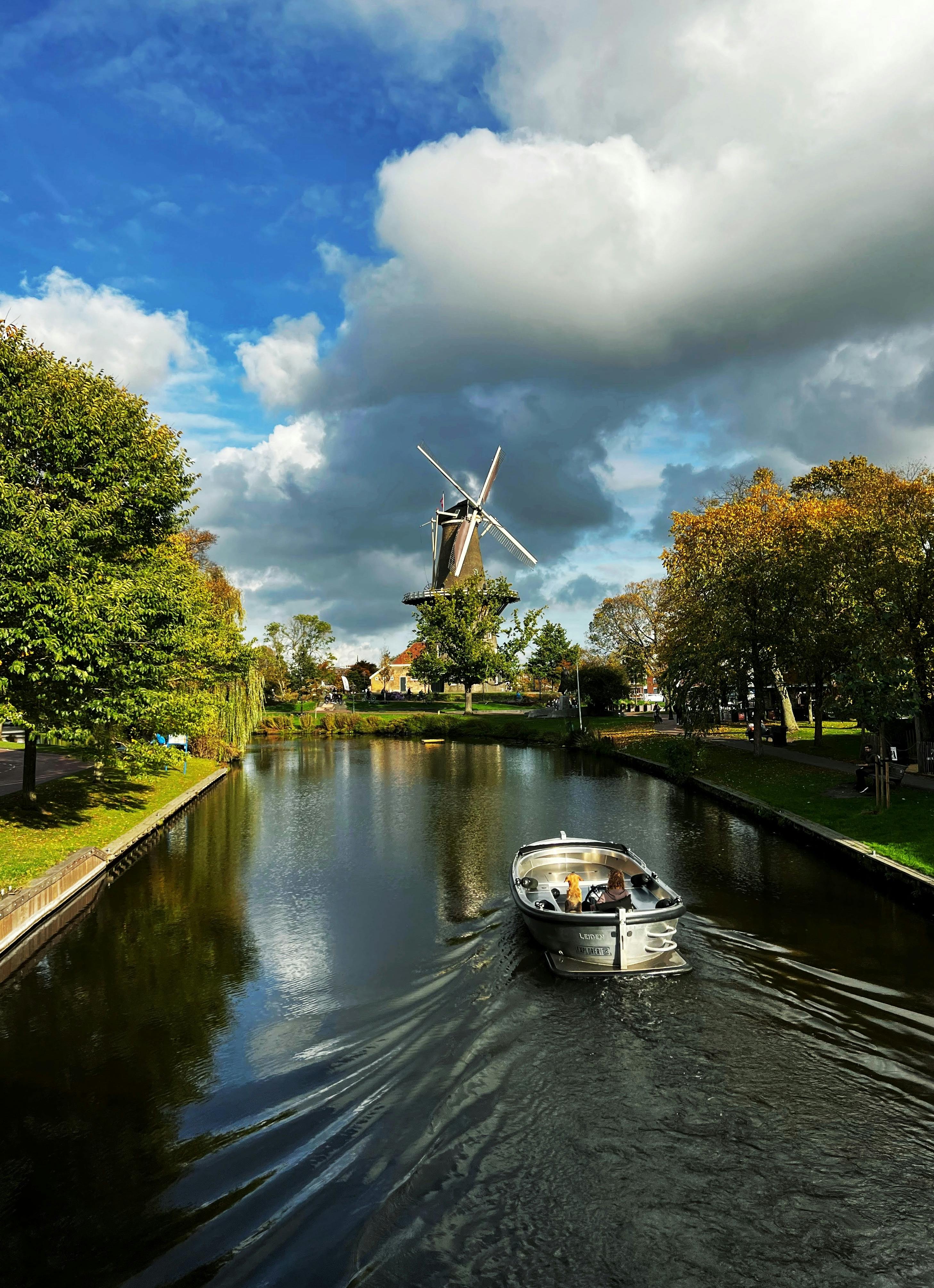 A boat traveling down a canal next to a windmill · Free Stock Photo