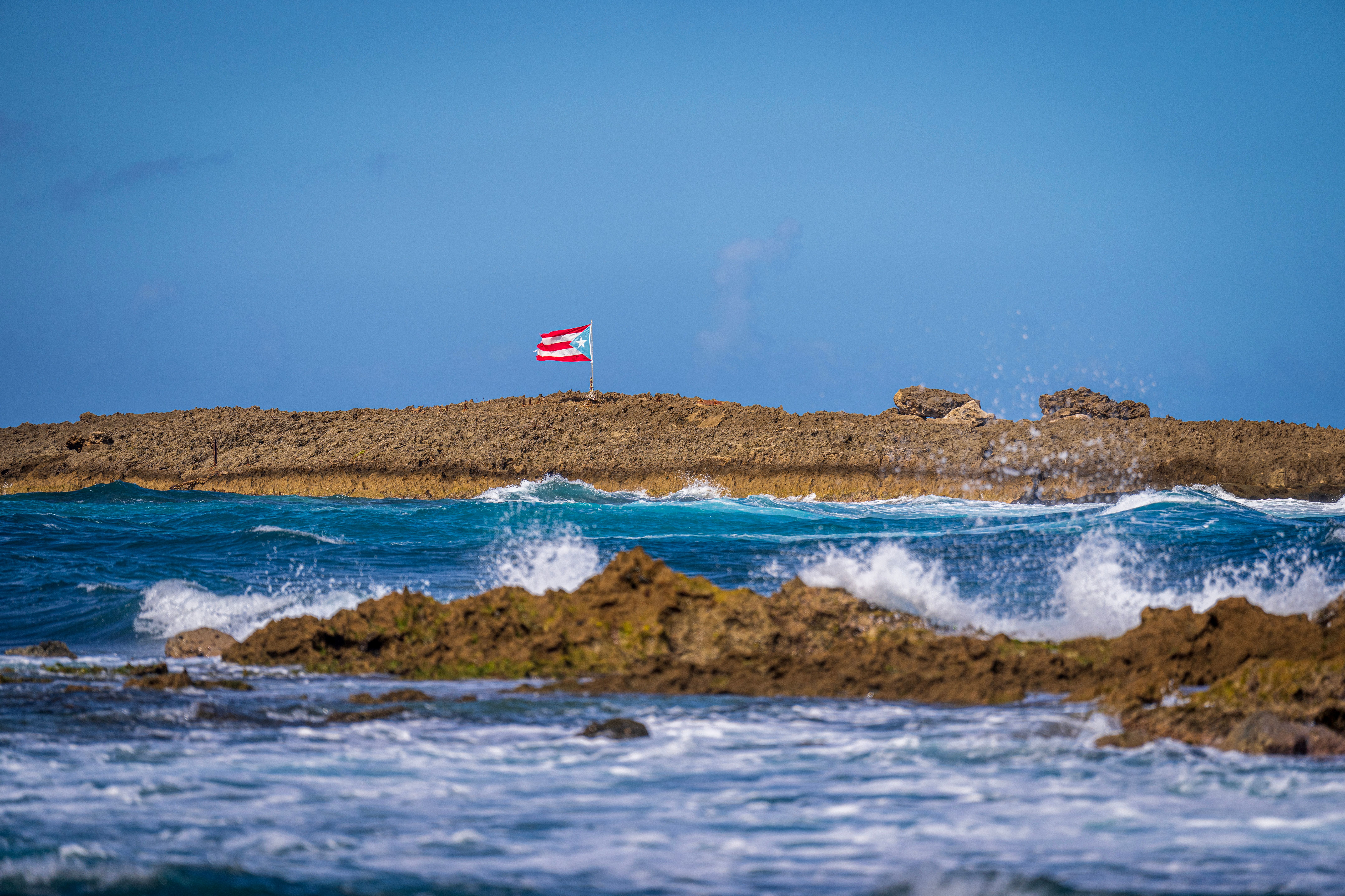 Porto Rican Flag on Rocks on Sea Shore · Free Stock Photo