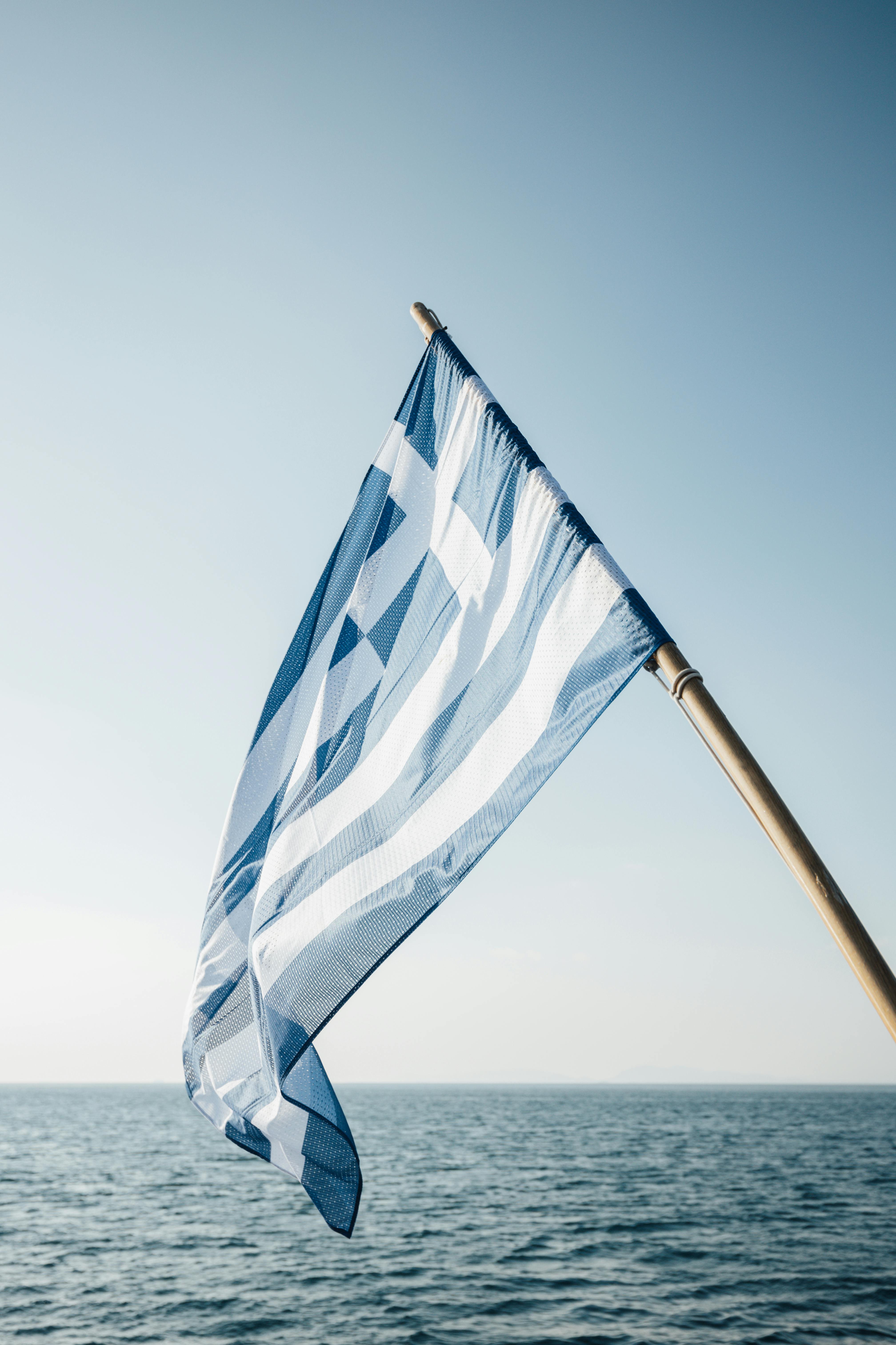 Greek Flag Waving Over Aegean Sea on Sunny Day · Free Stock Photo