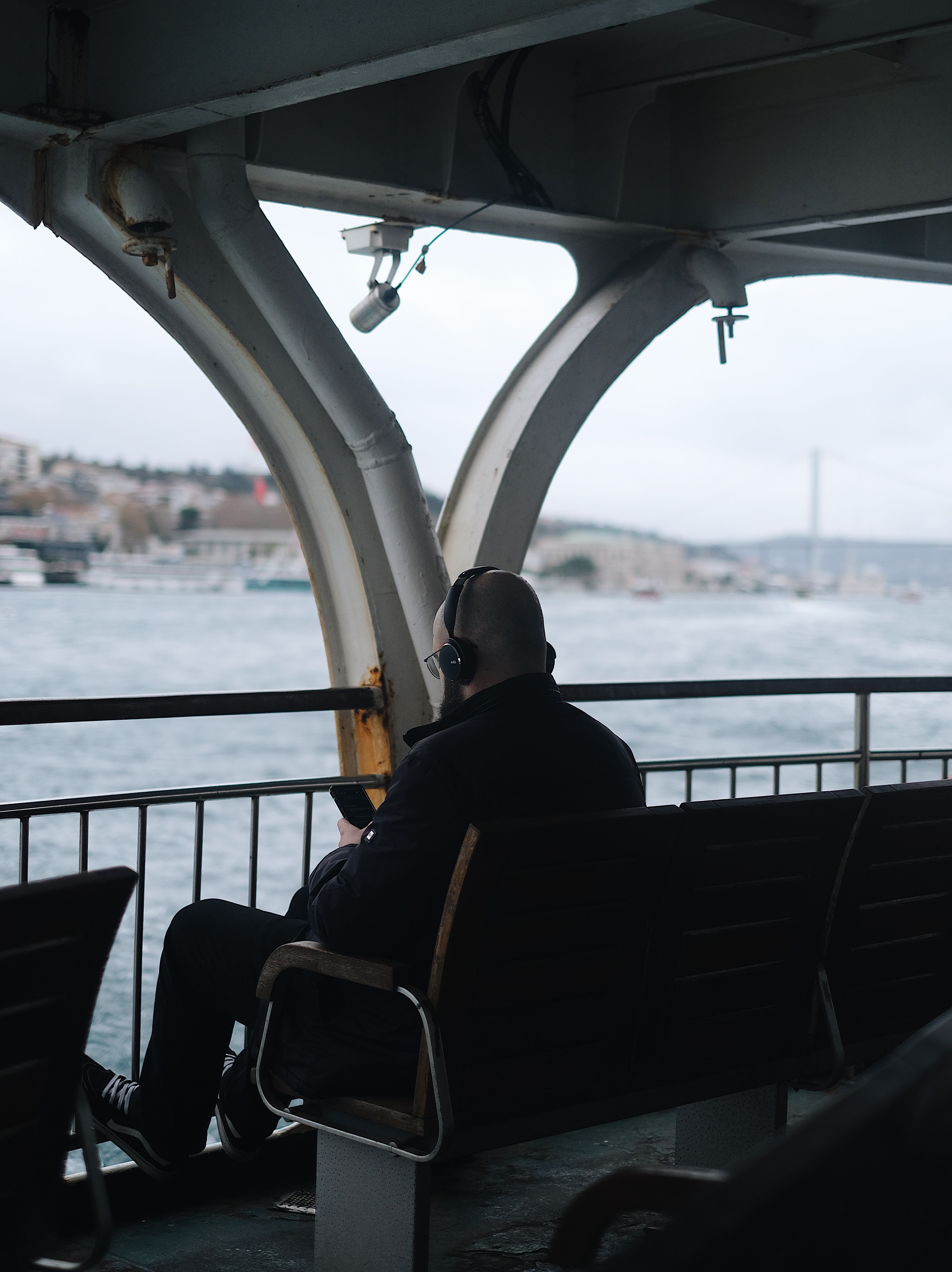 Back View of a Man Wearing a Hood, Sitting on a Ferry and Looking at ...