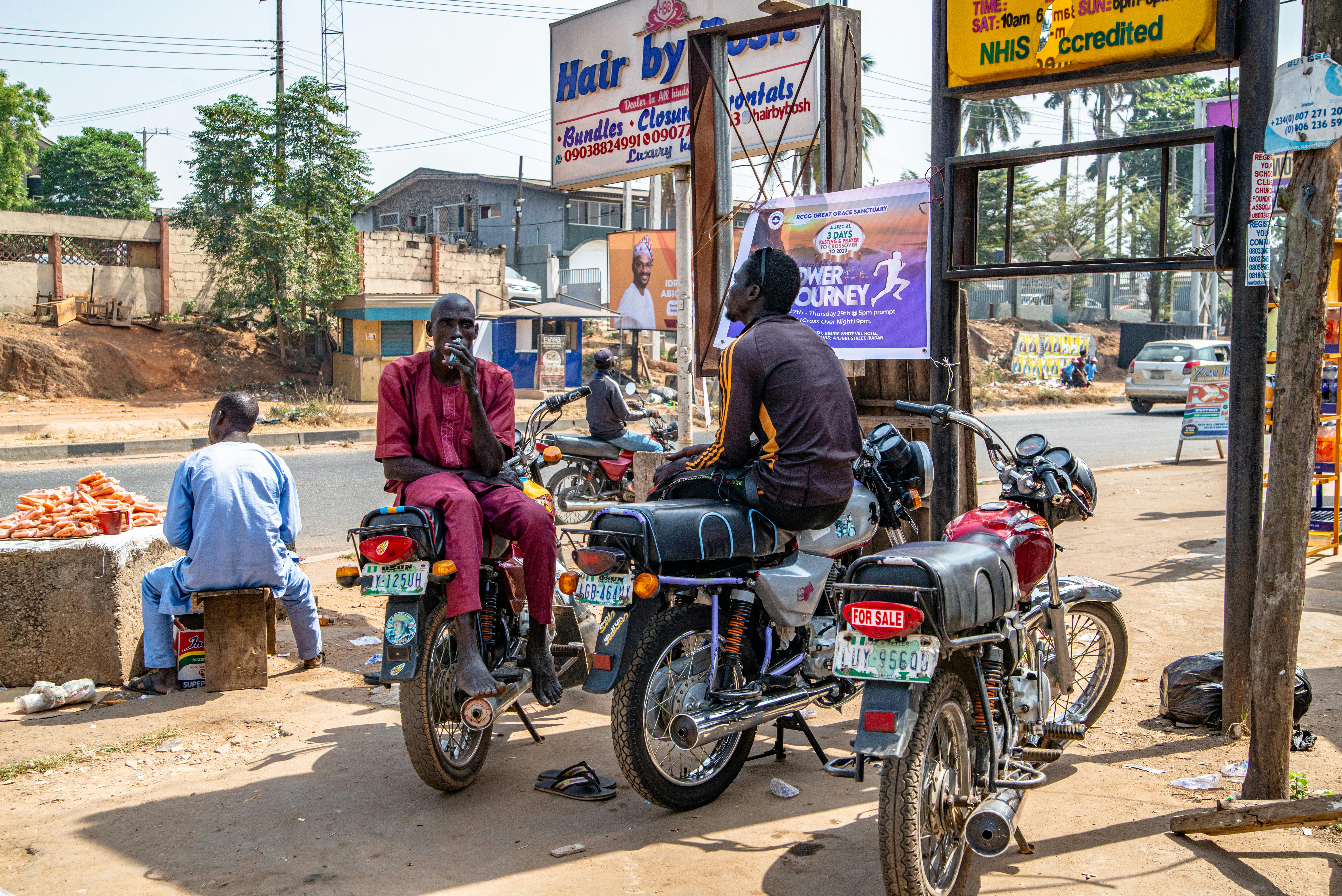 Men Sitting on Parked Motorcycles Behind a Street Vendor in an Nigerian ...