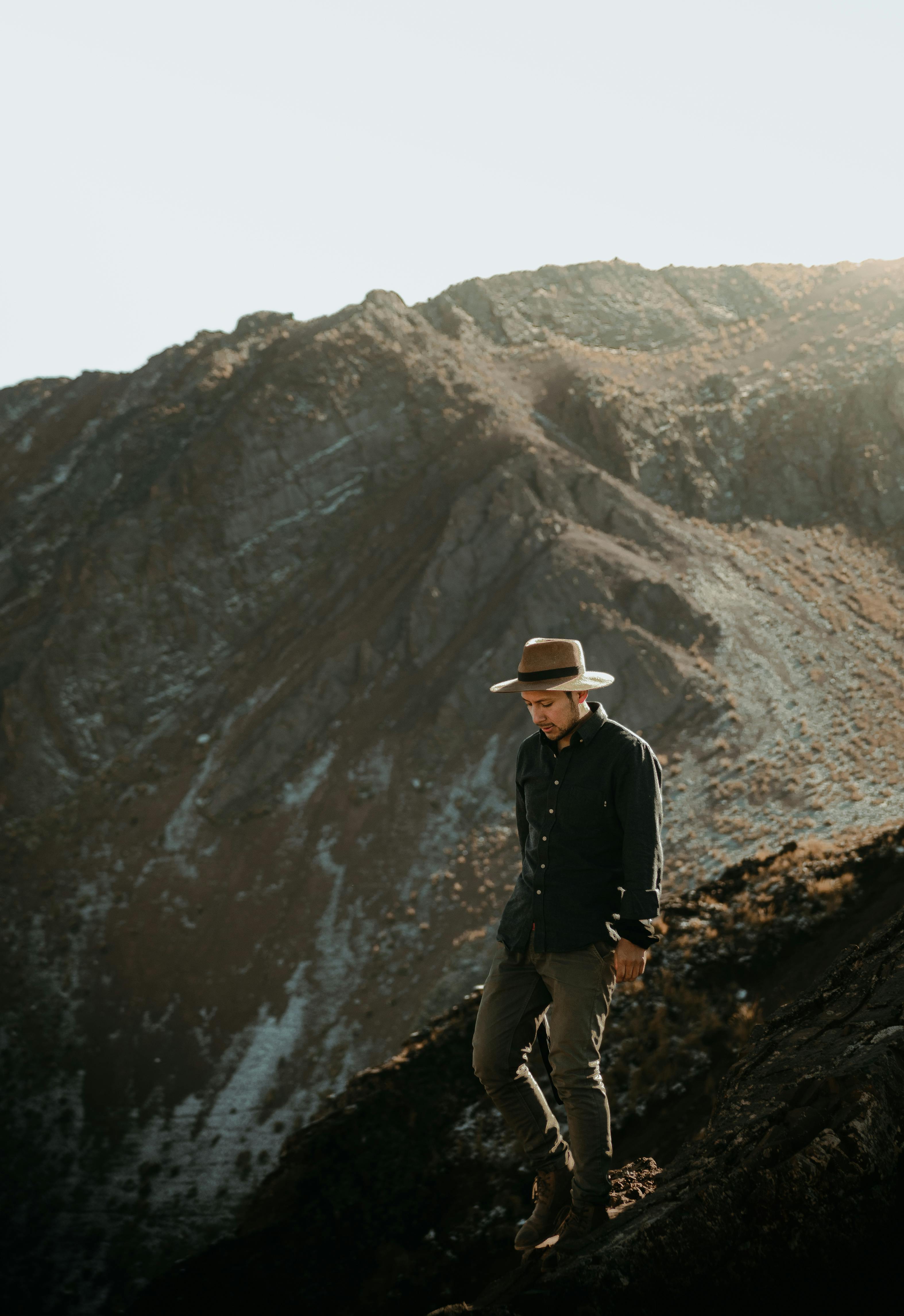 Man Wearing Hat Walking along Mountain Top · Free Stock Photo