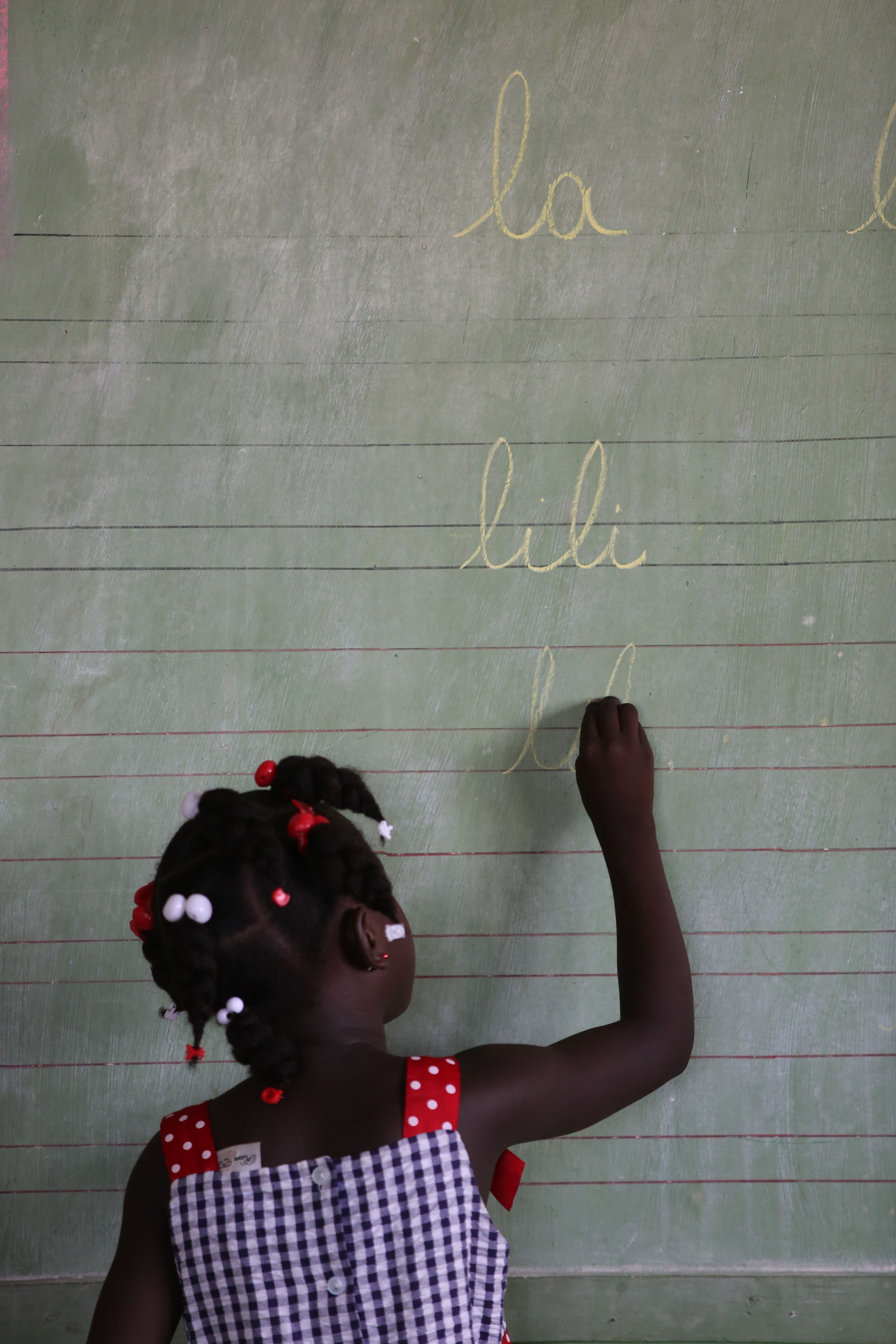 Back View of a Child Writing on a Blackboard · Free Stock Photo