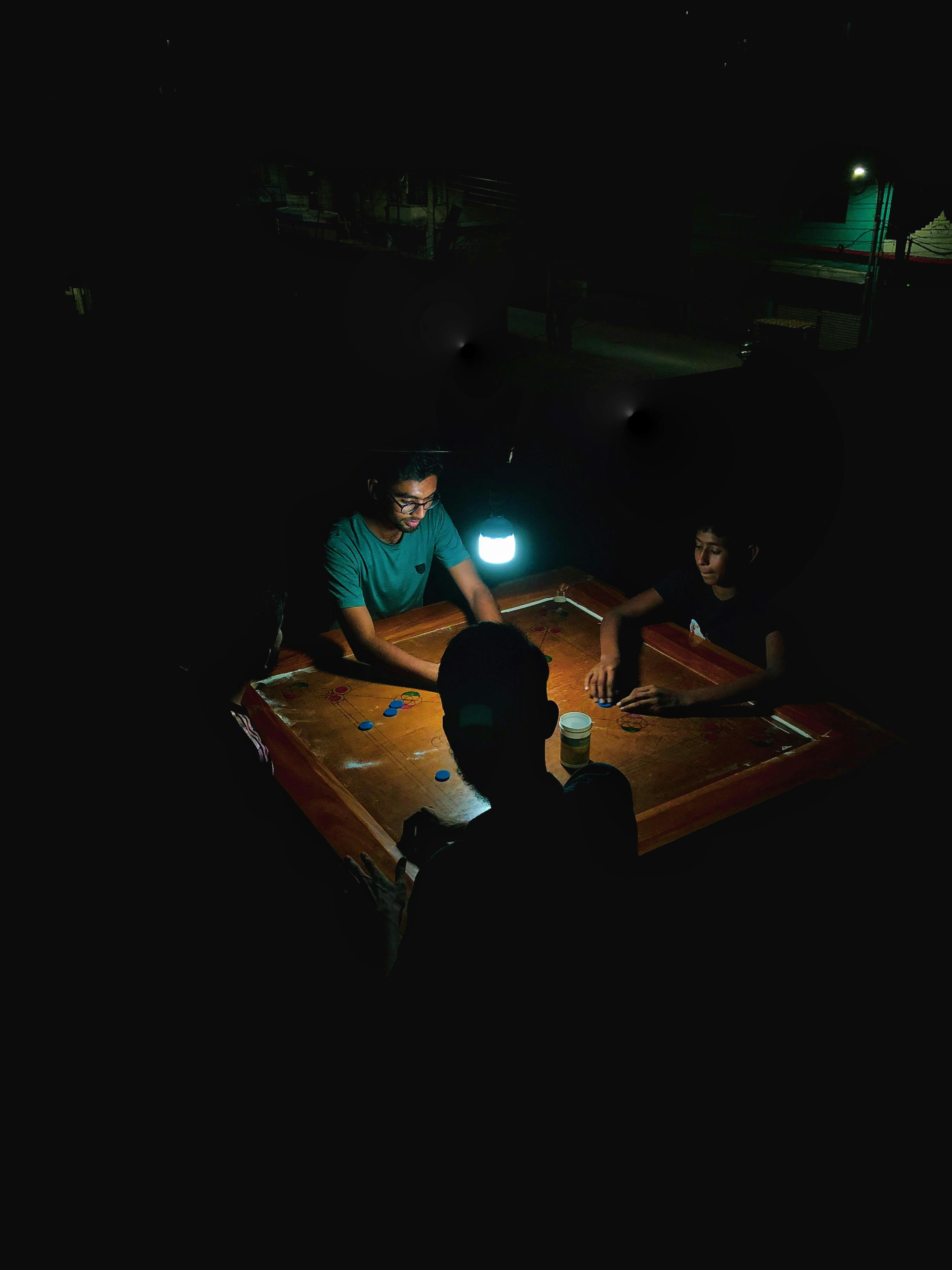 Men Sitting by Table in Darkness and Playing · Free Stock Photo