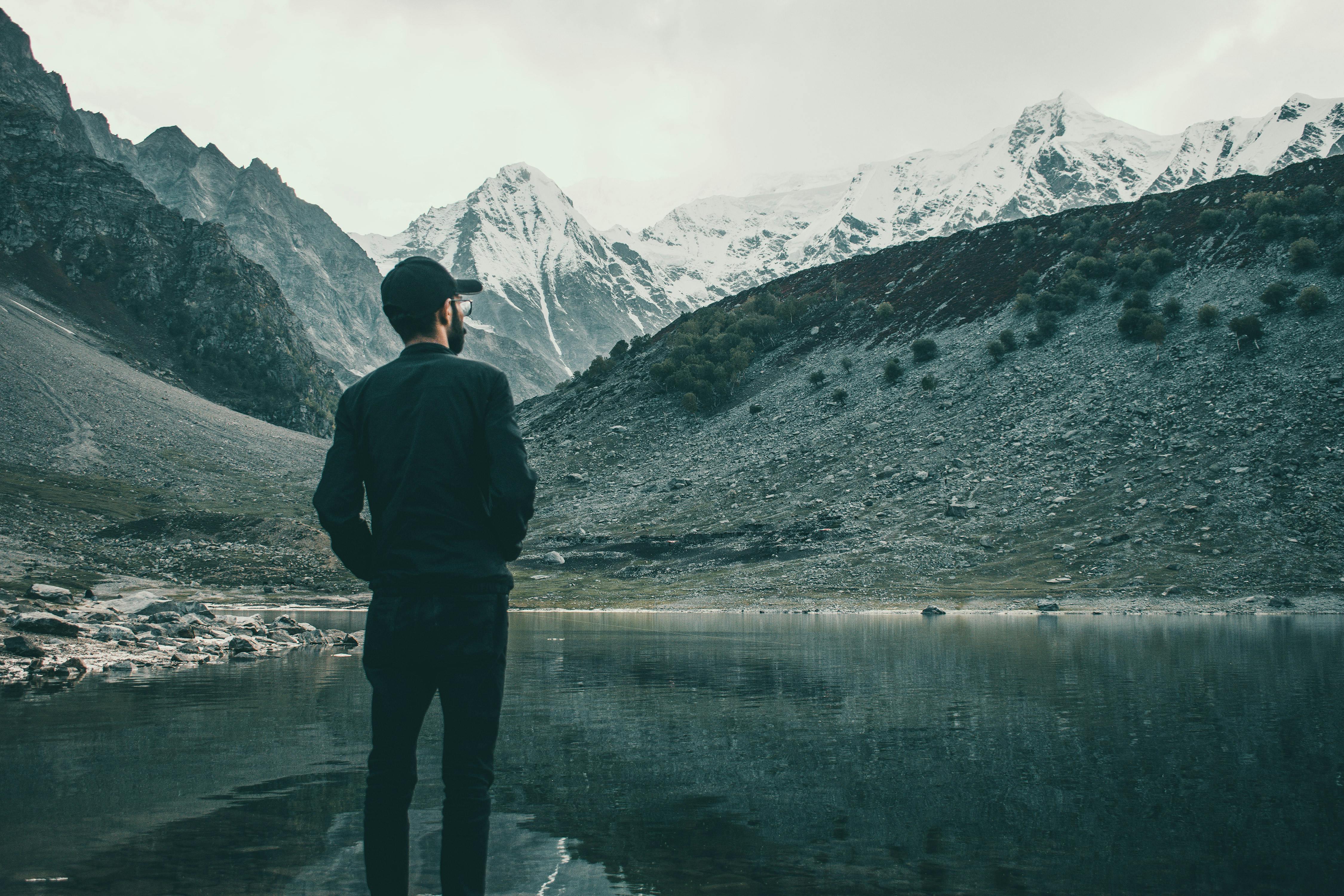 Back View of a Man Standing by a Lake in a Valley and Looking at Rocky ...