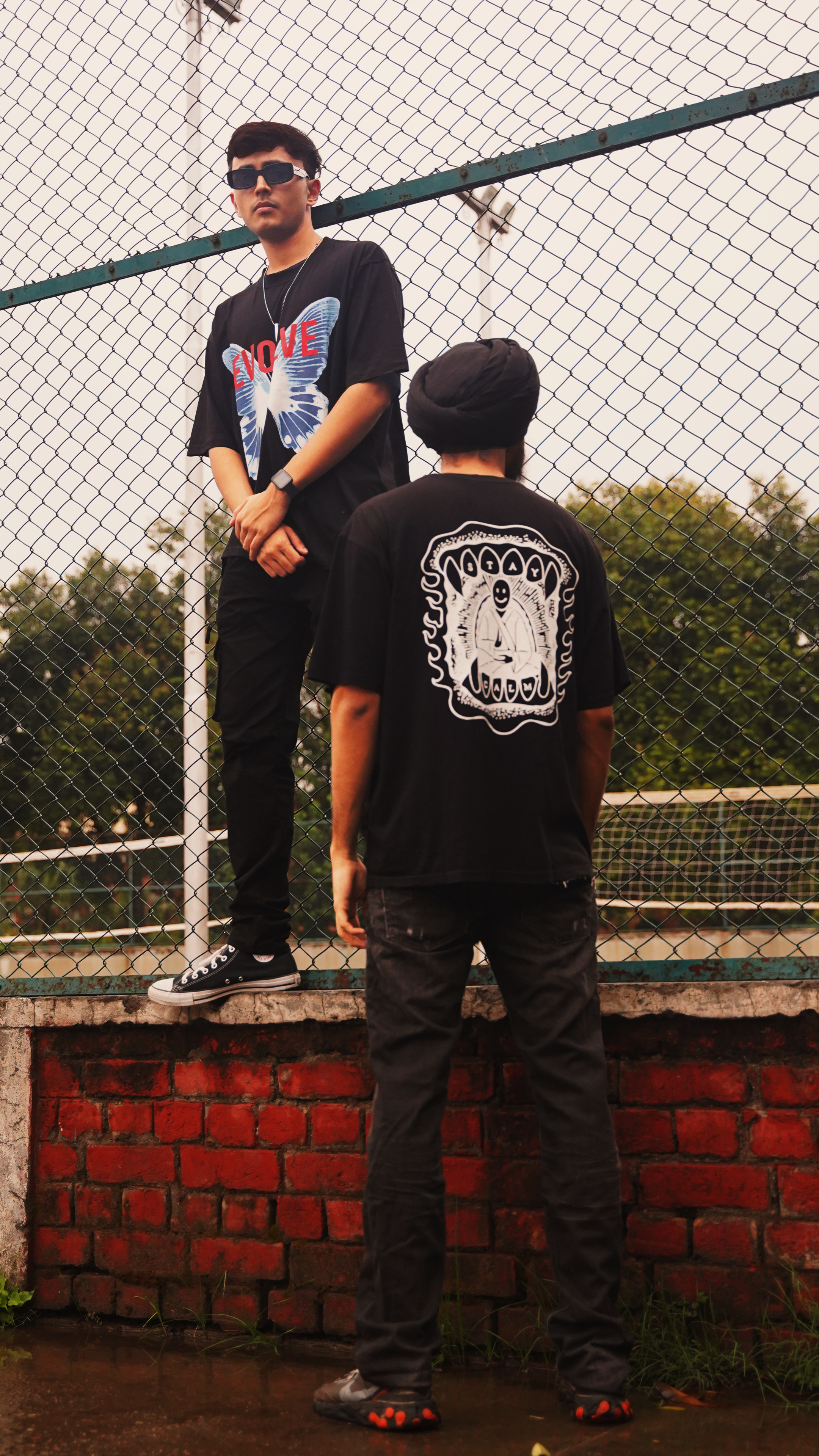 Two Men Standing near a Fence, Wearing Graphic T-shirts and Sunglasses ...