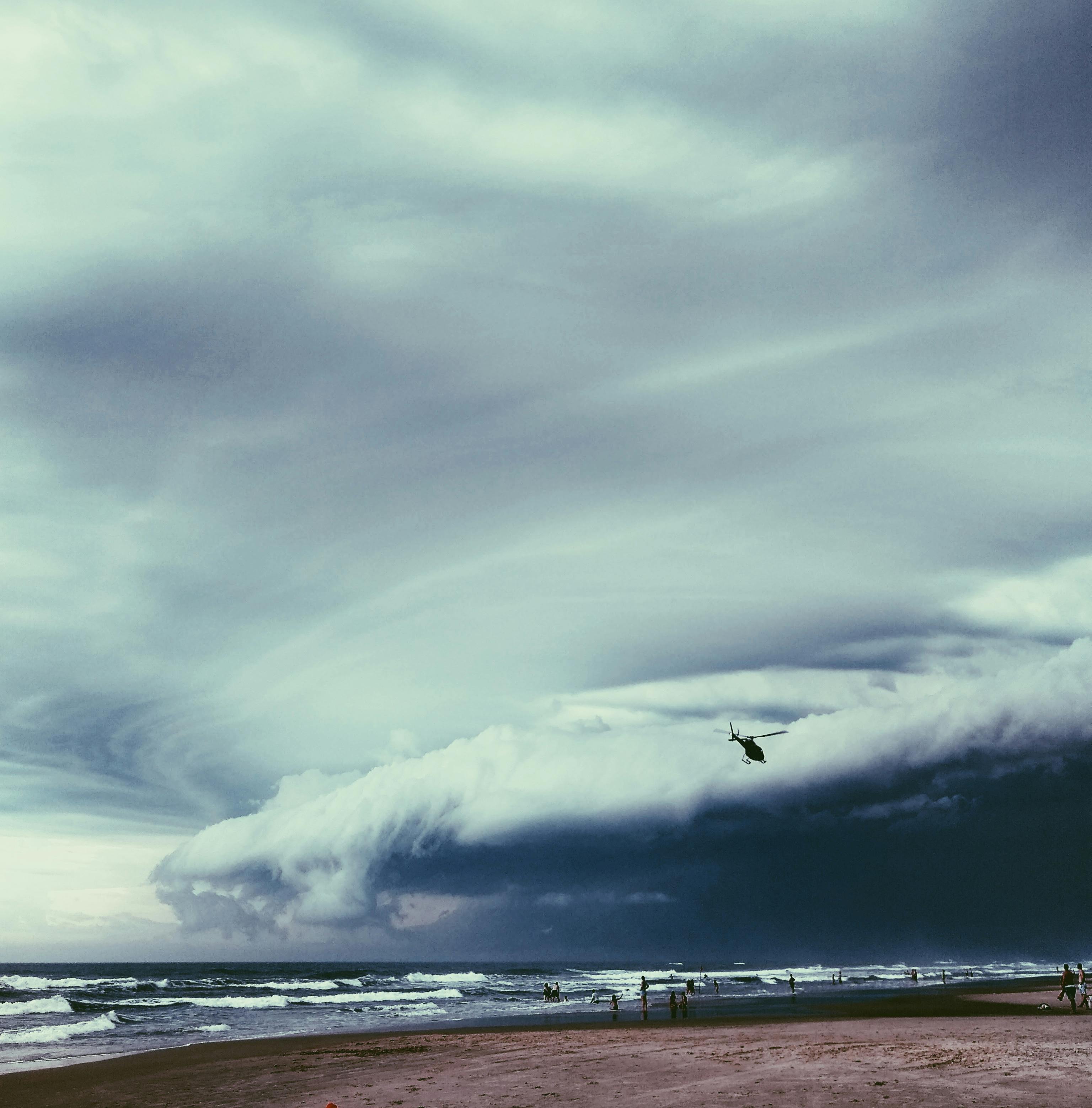 Helicopter Flying over a Beach, under a Dark Storm Cloud · Free Stock Photo