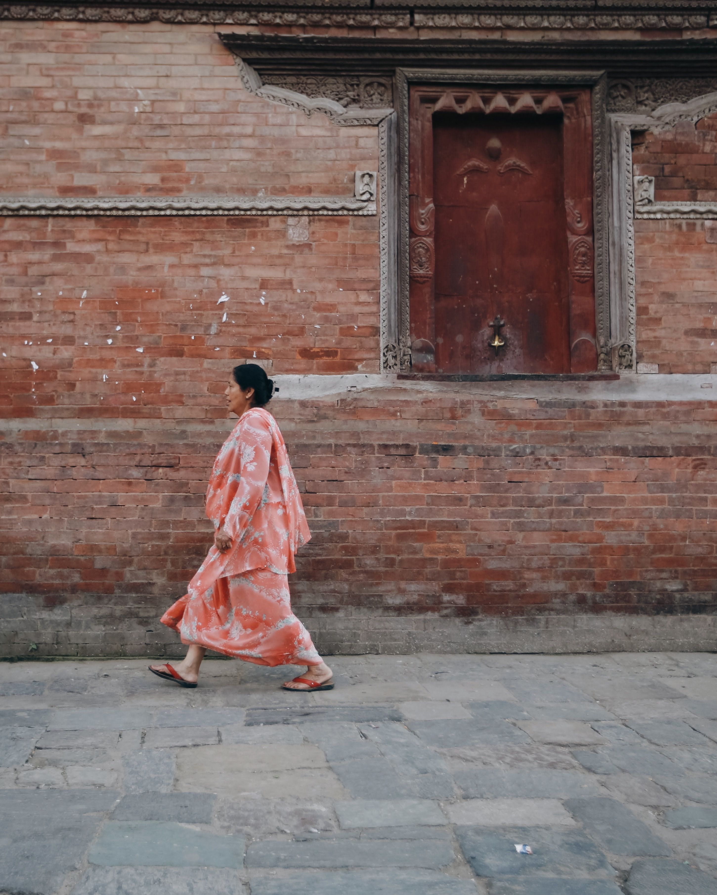 Woman in Traditional Clothes Walking near Brick Wall · Free Stock Photo