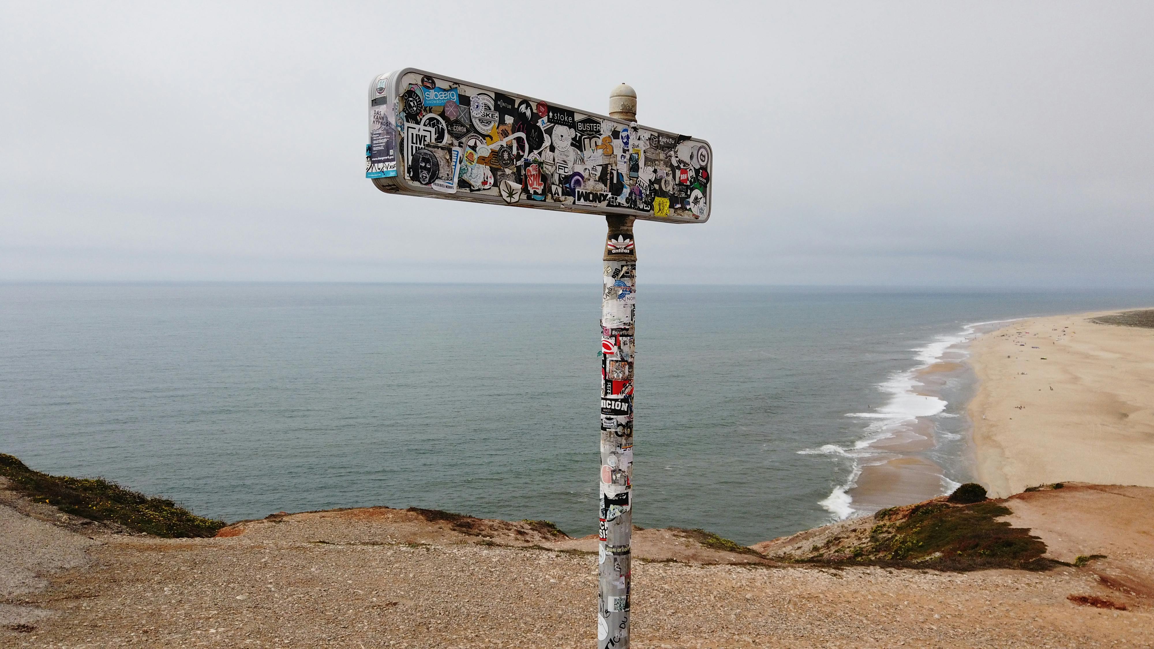 Coastline and Sign with Stickers on it · Free Stock Photo