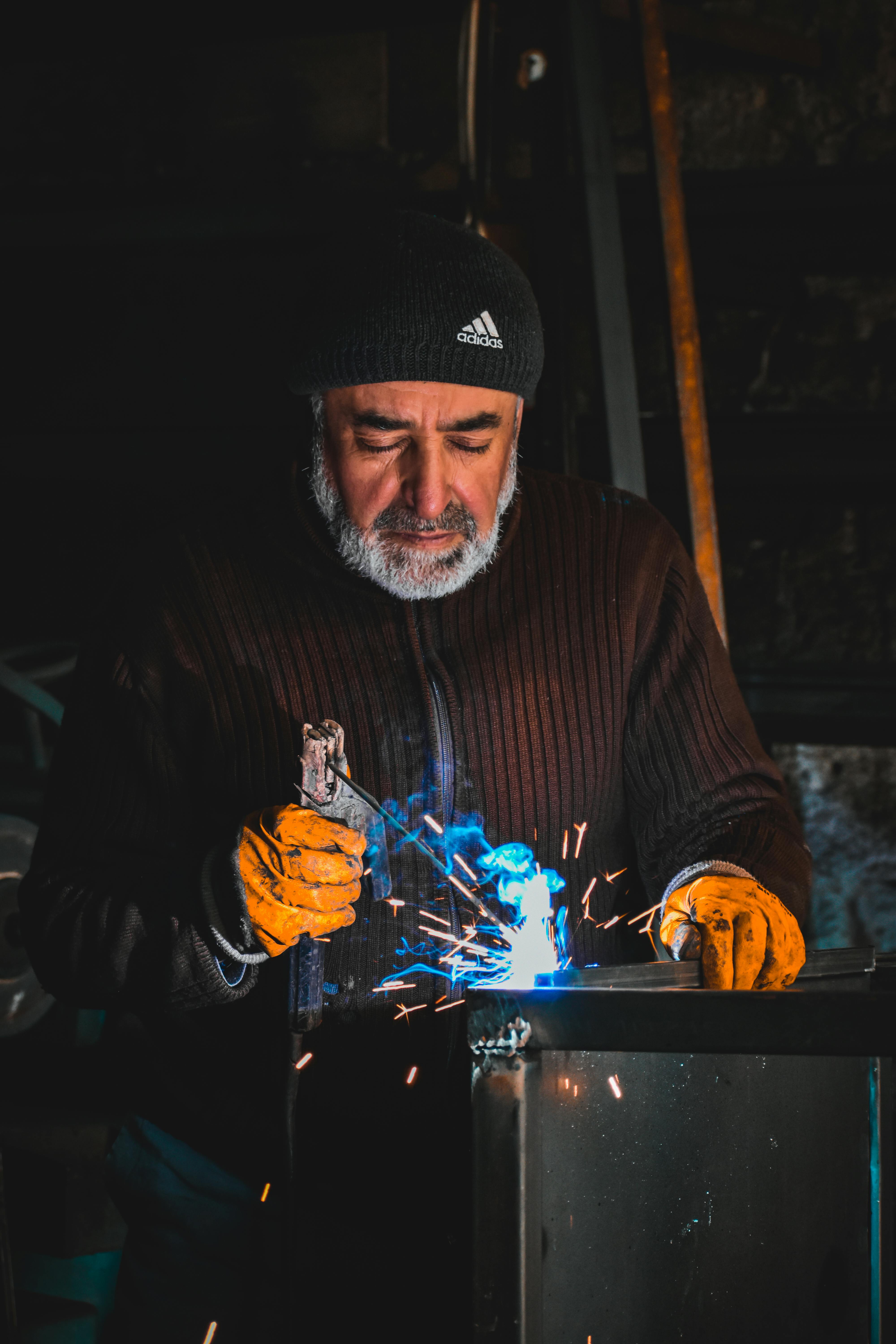 Old Bearded Man Welding Metal in Dark · Free Stock Photo
