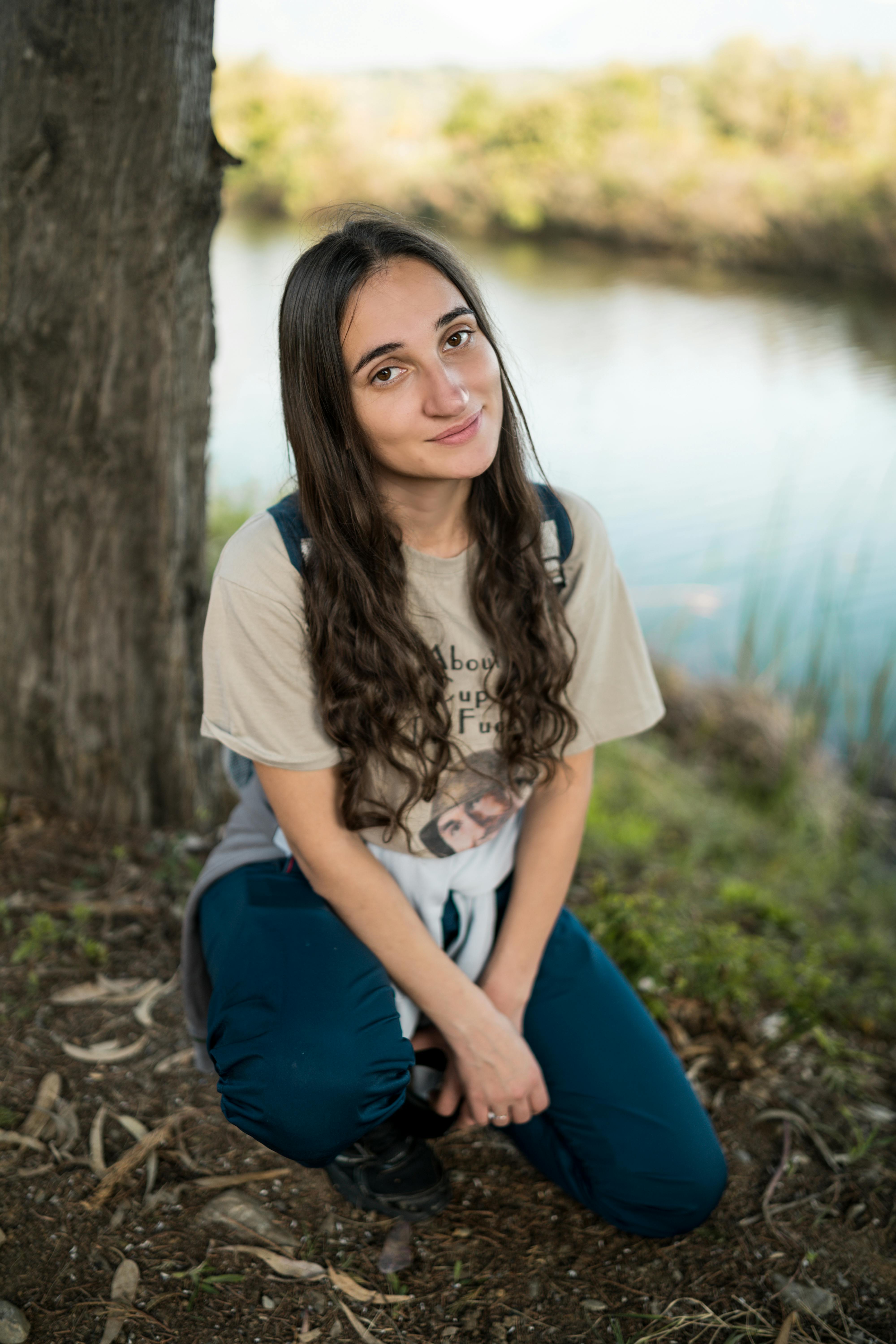Smiling Woman Crouching near Tree and Water · Free Stock Photo