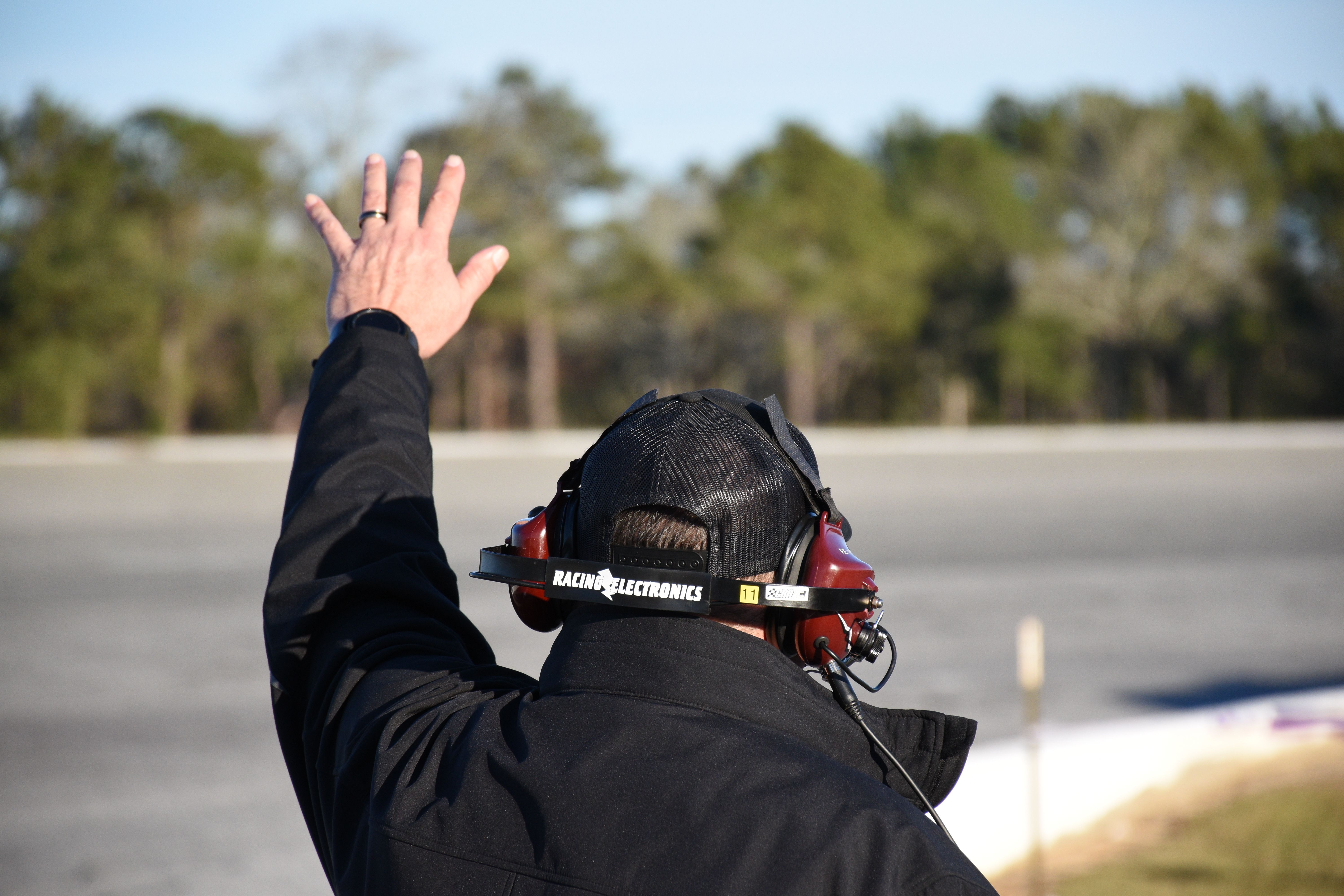 Back View of a Man Standing next to a Race Track with His Hand Raised ...