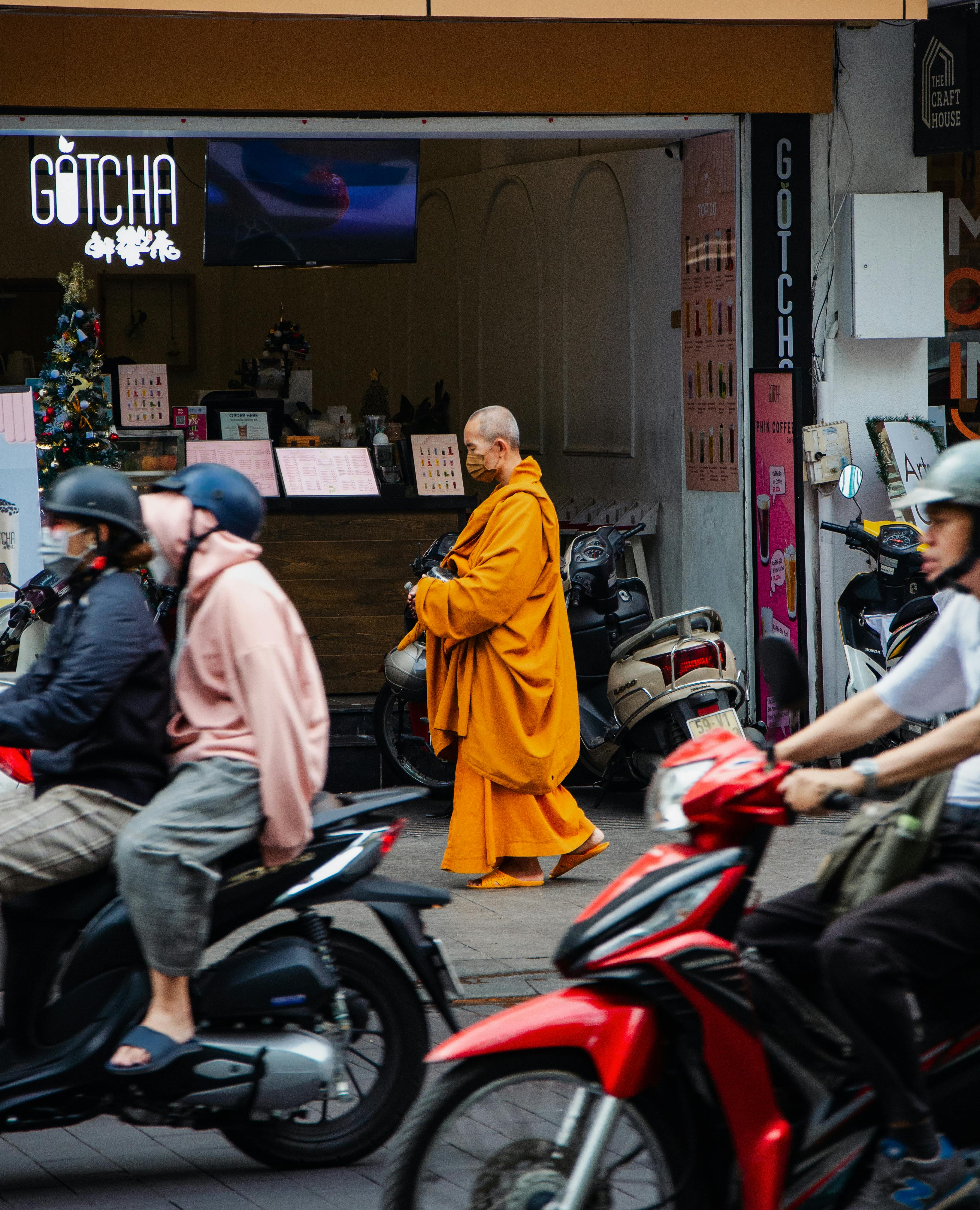 Buddhist Monk Walking near Scooters on Street · Free Stock Photo