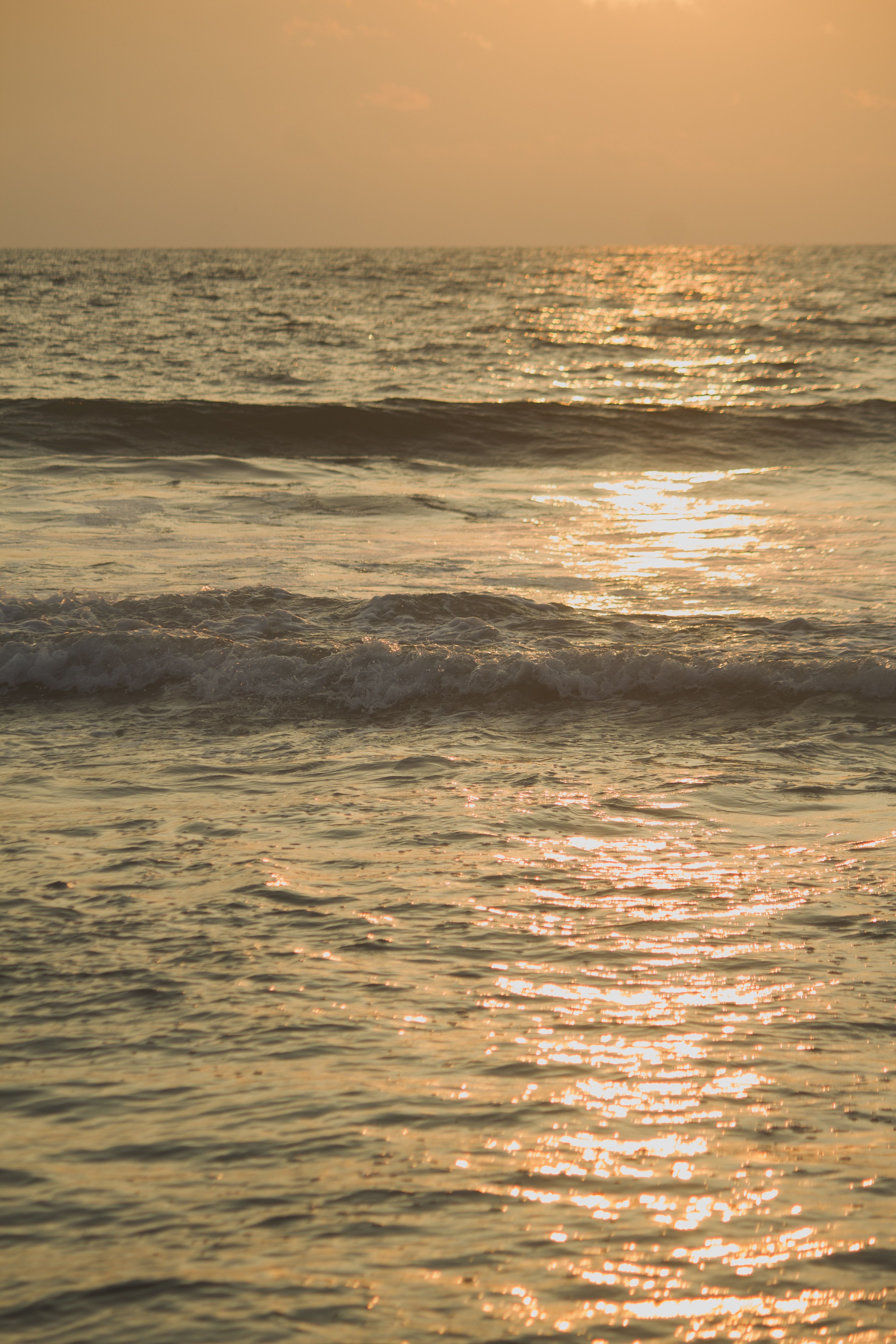 A sunset over the ocean with waves and a surfboard · Free Stock Photo