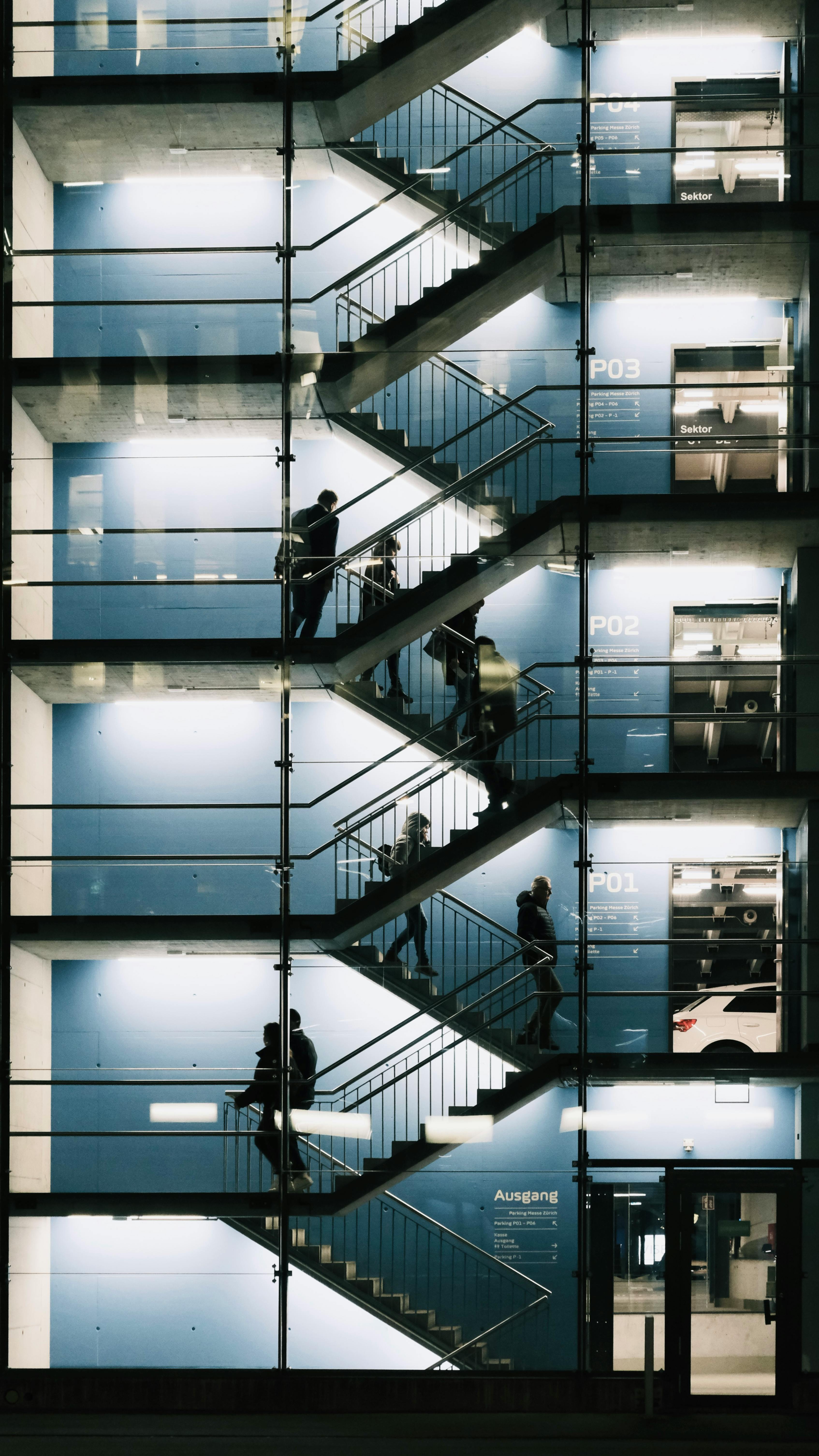 People Walking on Stairs behind Parking Lot Window · Free Stock Photo