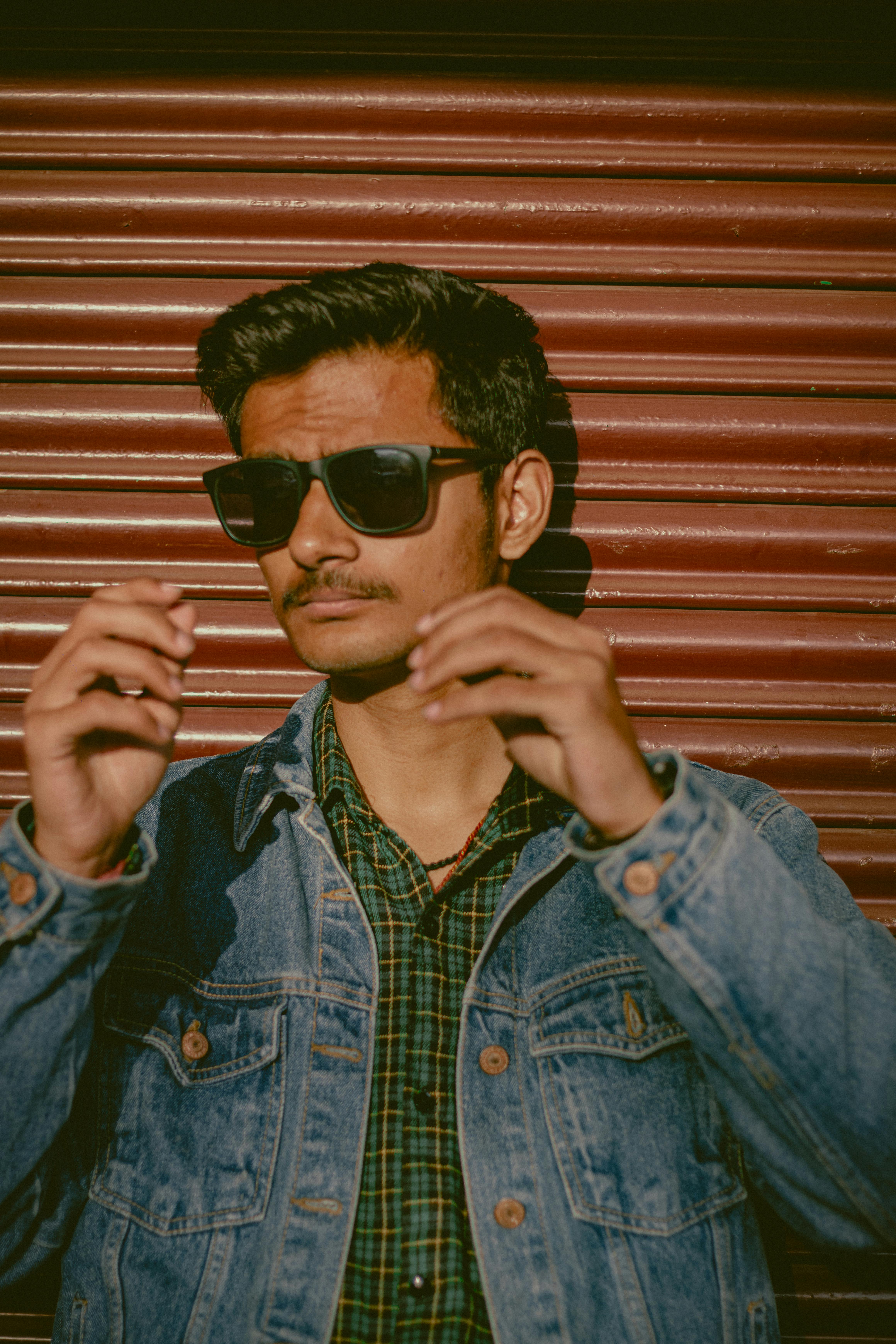 Standing Man in Denim Jacket Reaching for Shades · Free Stock Photo