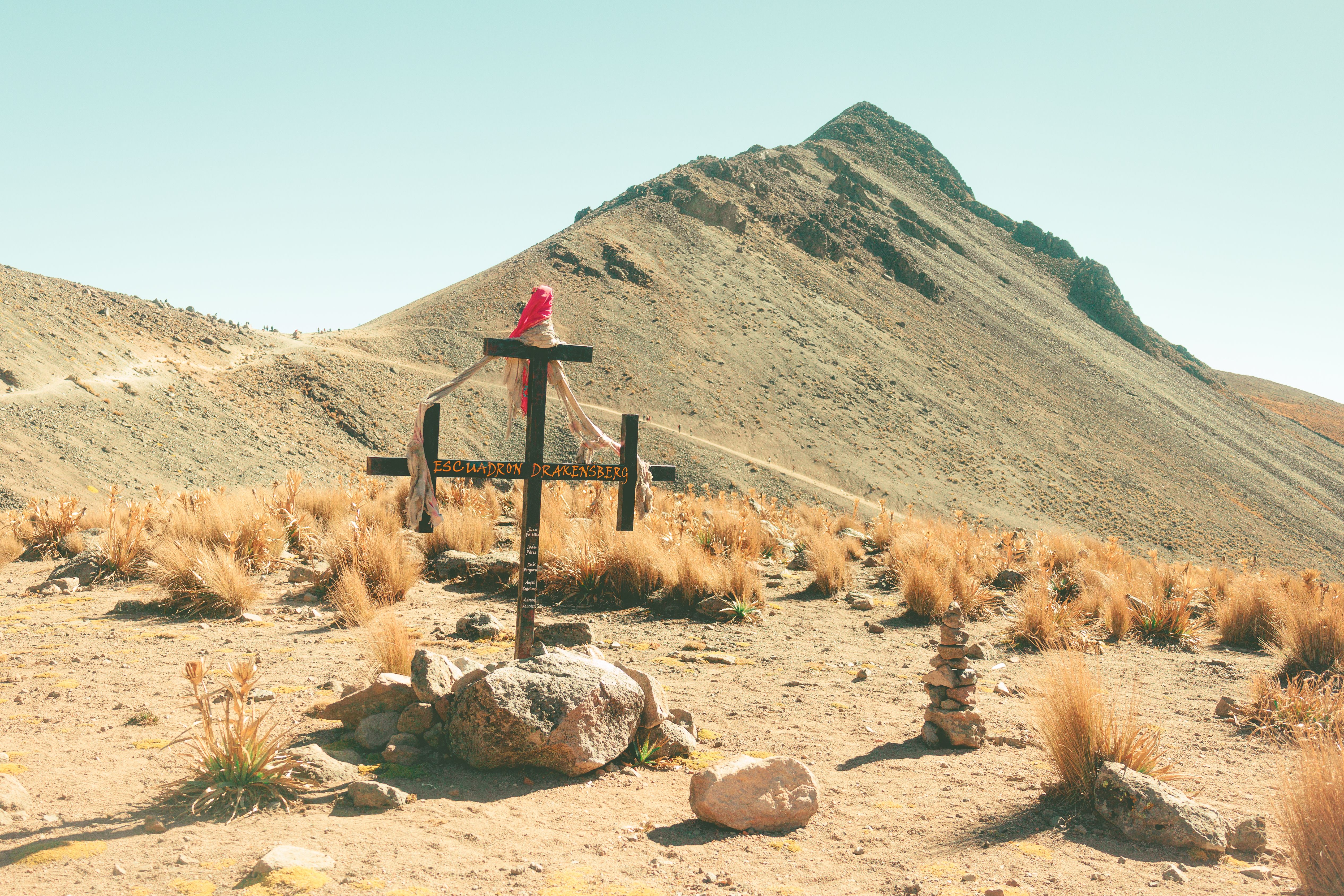 A cross in the middle of a desert with mountains in the background ...
