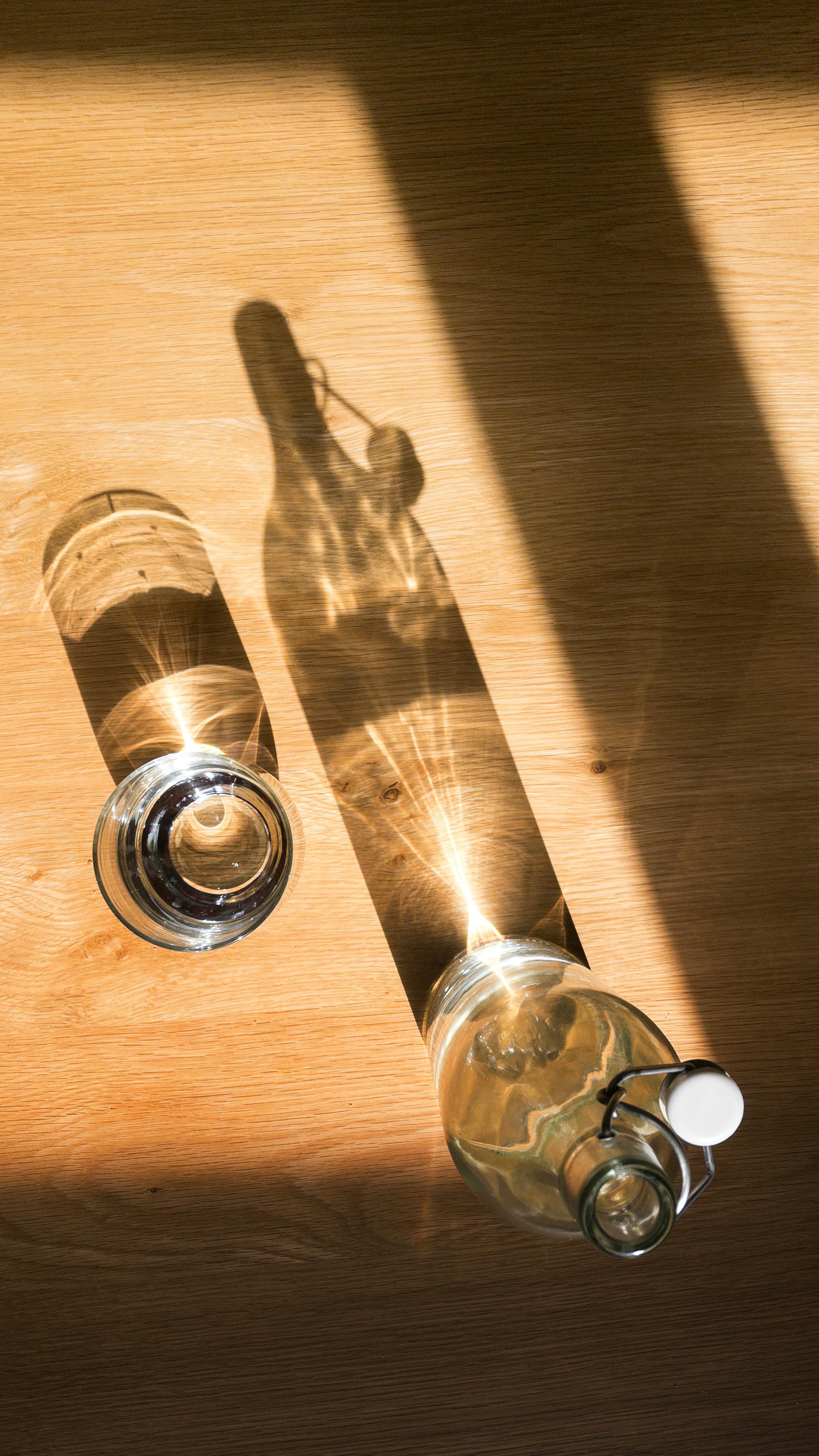 A Bottle and a Glass Casting Shadows on a Table · Free Stock Photo