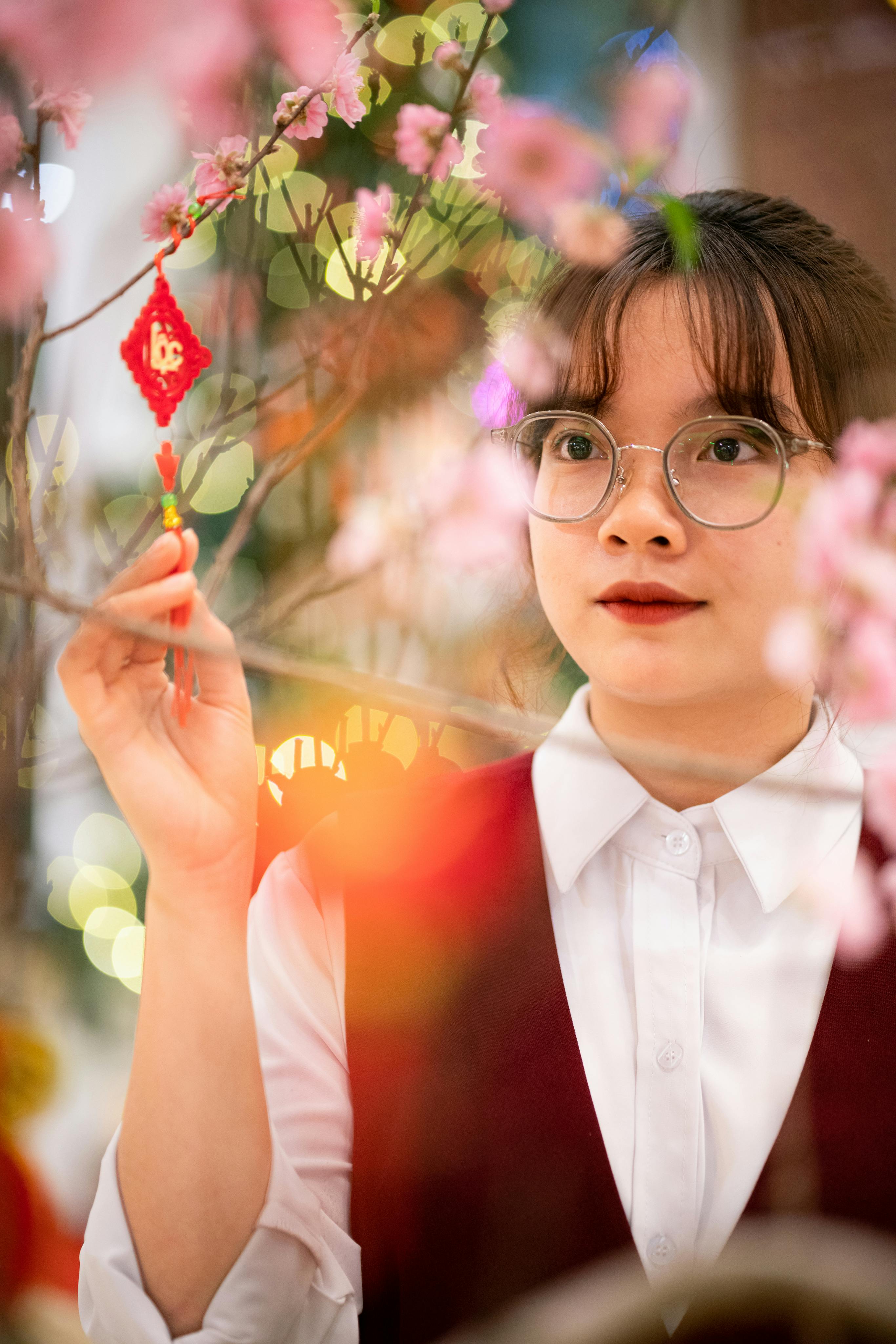 Girl in Glasses Hanging Traditional Decor on Blooming Tree · Free Stock Photo