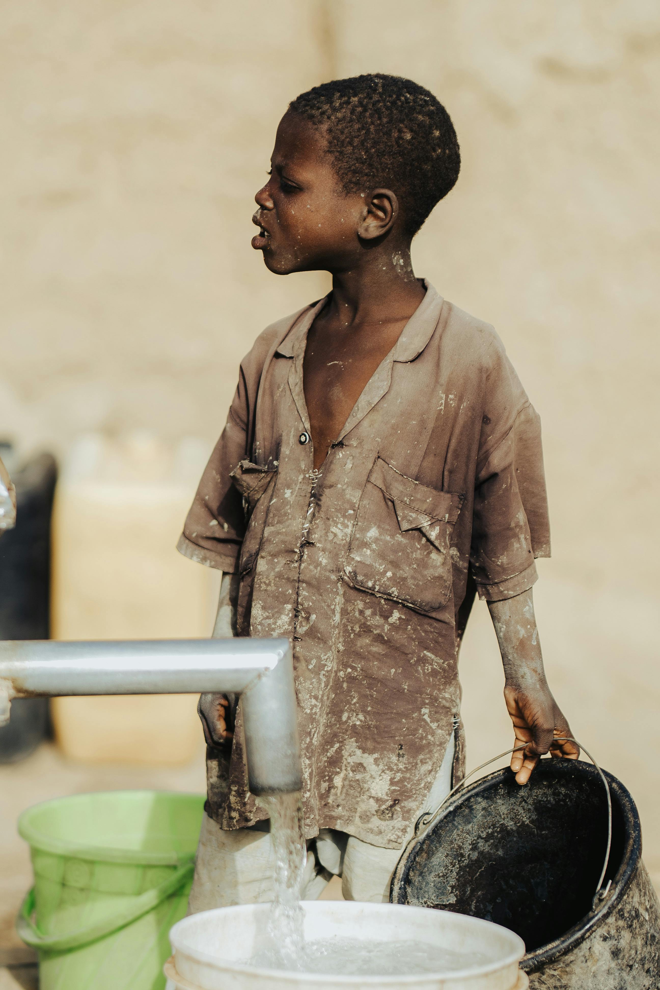A Boy in Dirty Clothing with a Bucket · Free Stock Photo
