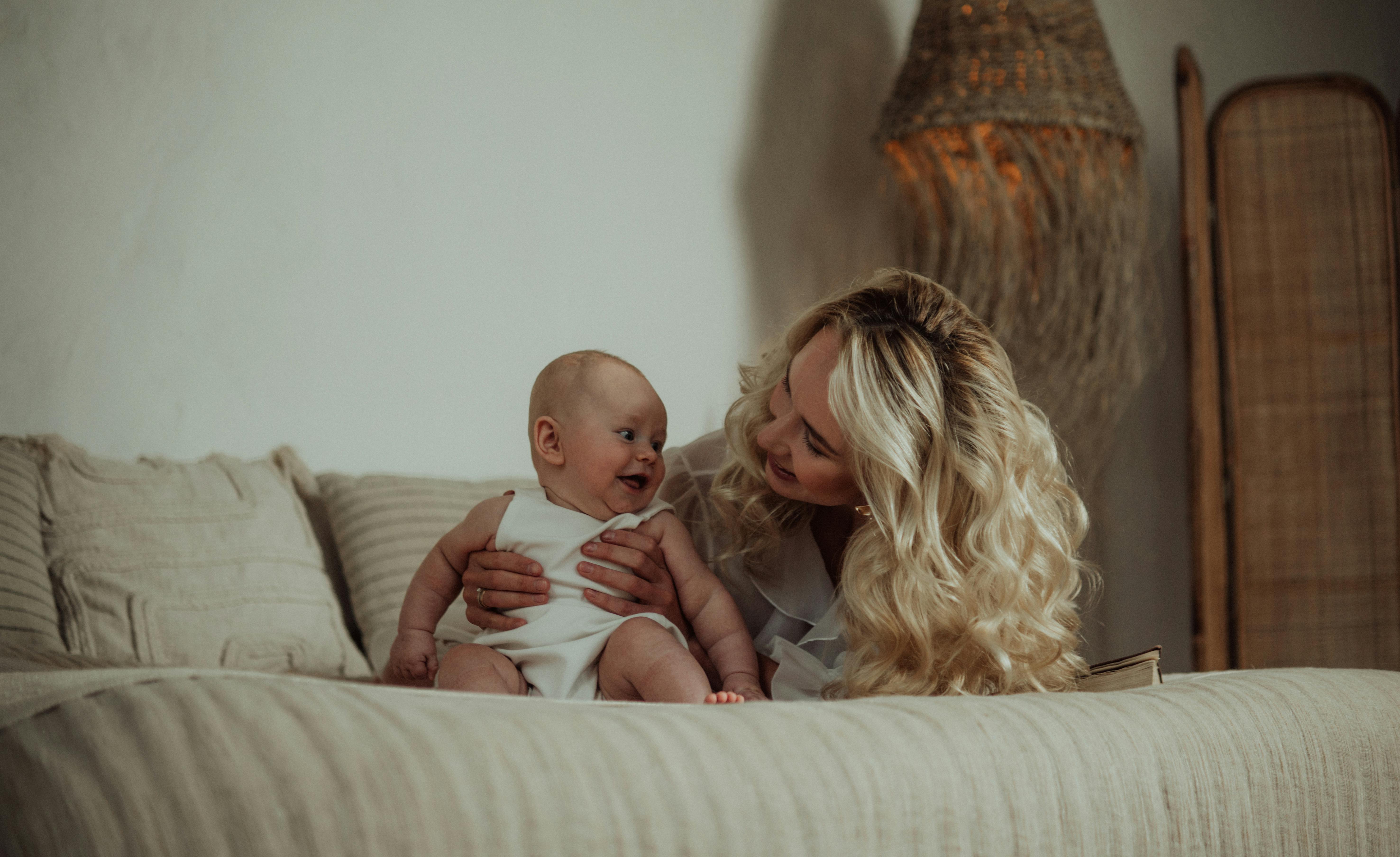 Photo of a Smiling Woman with a Baby Sitting on a Bed · Free Stock Photo